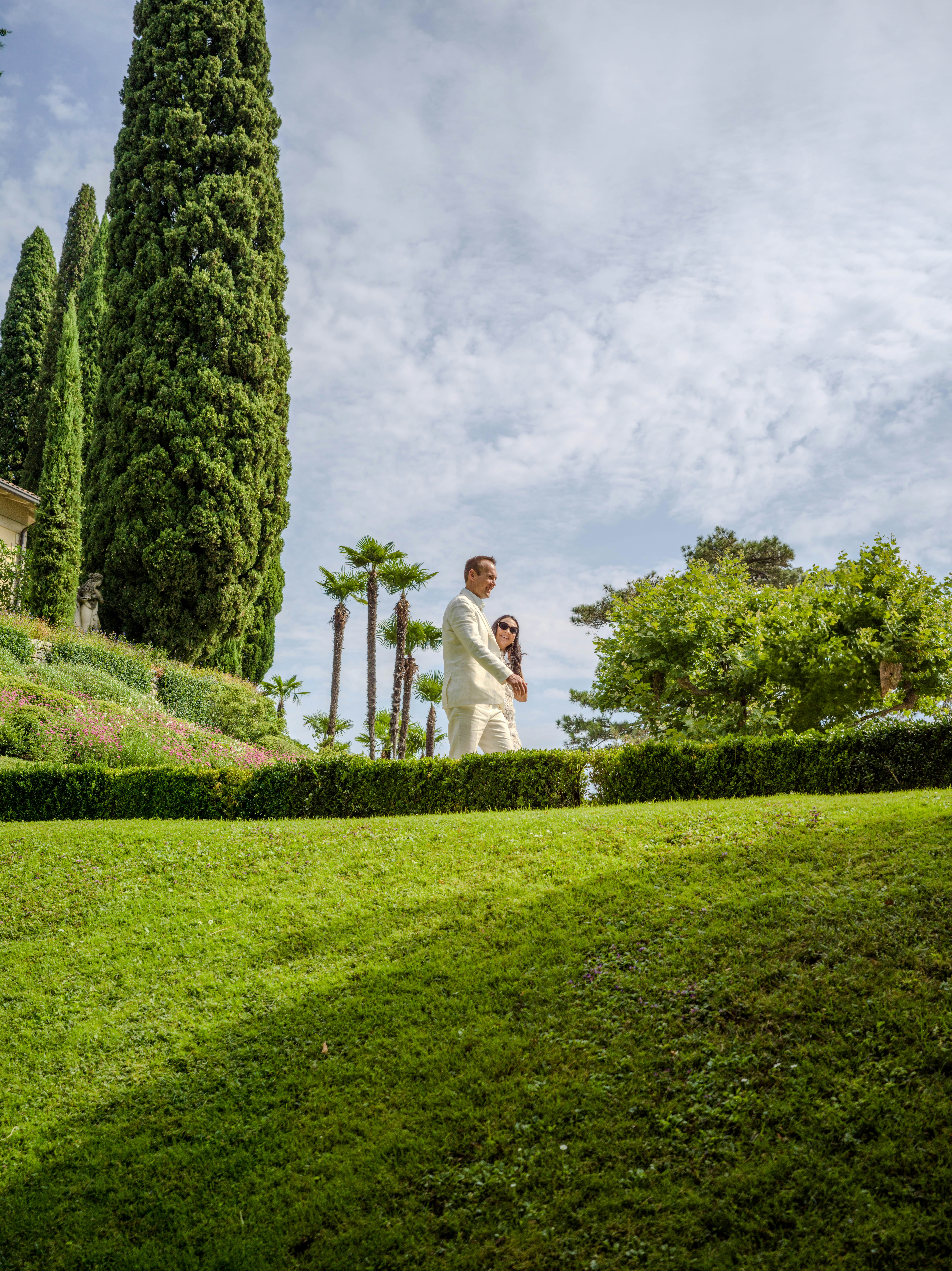White-suited couple strolling along a sunlit garden terrace