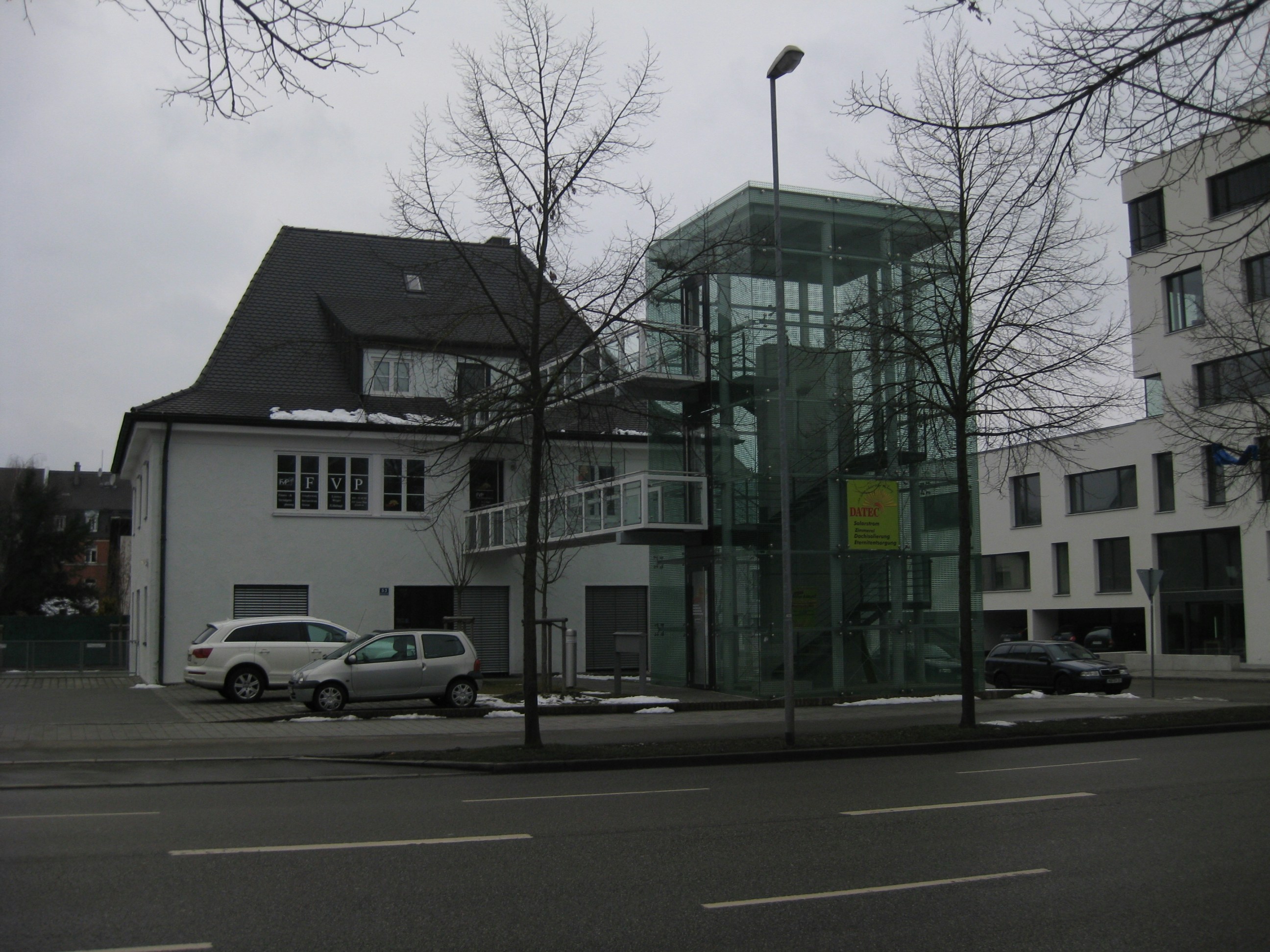 Modern glass elevator structure attached to white building.