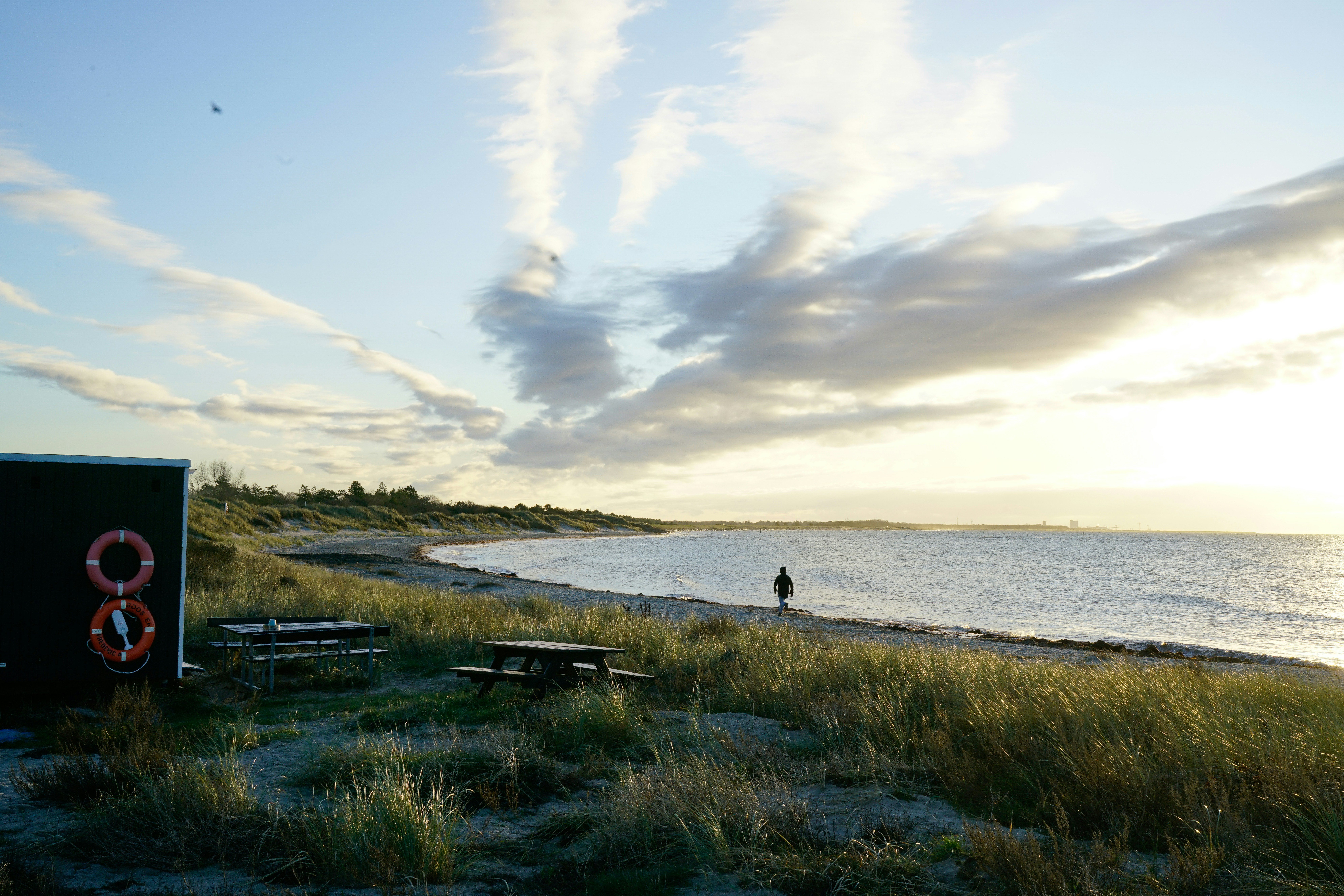 Shoreline Quiet: A lone figure at the edge of the water under expansive sky