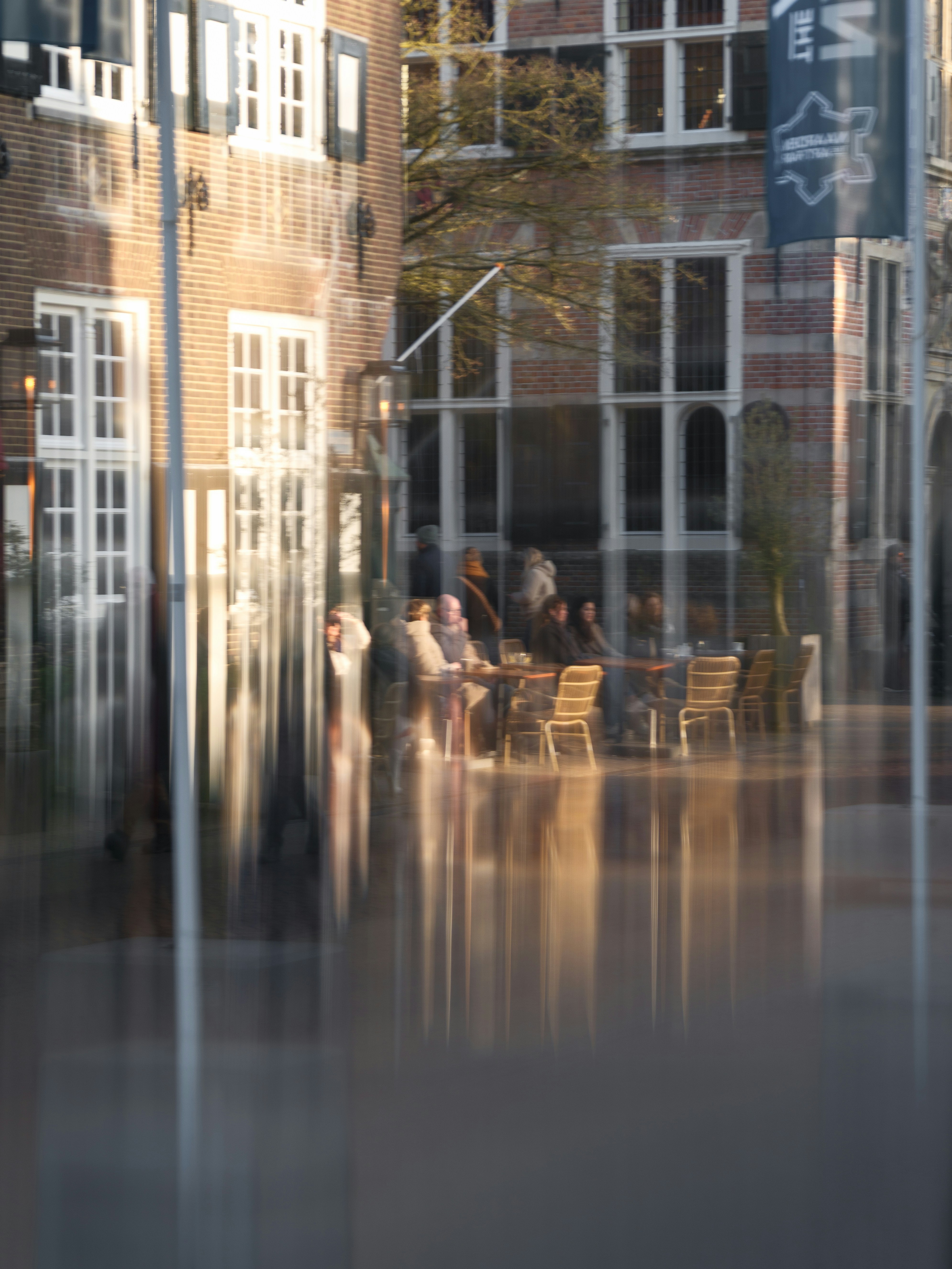 Cafe Reflections: Blurred Figures through a Glassy Courtyard