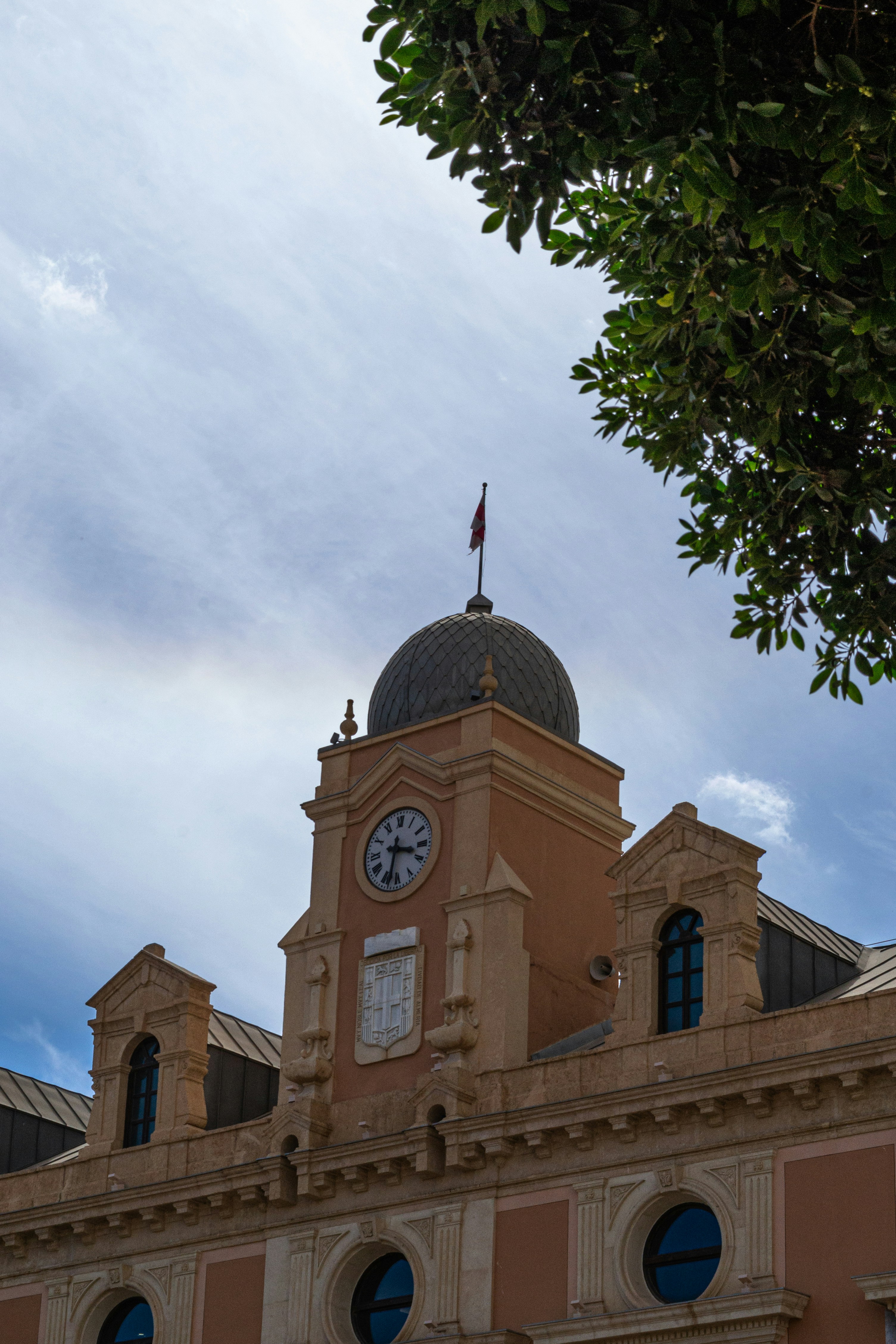 Clocktower atop peach-toned façade under a leafy canopy