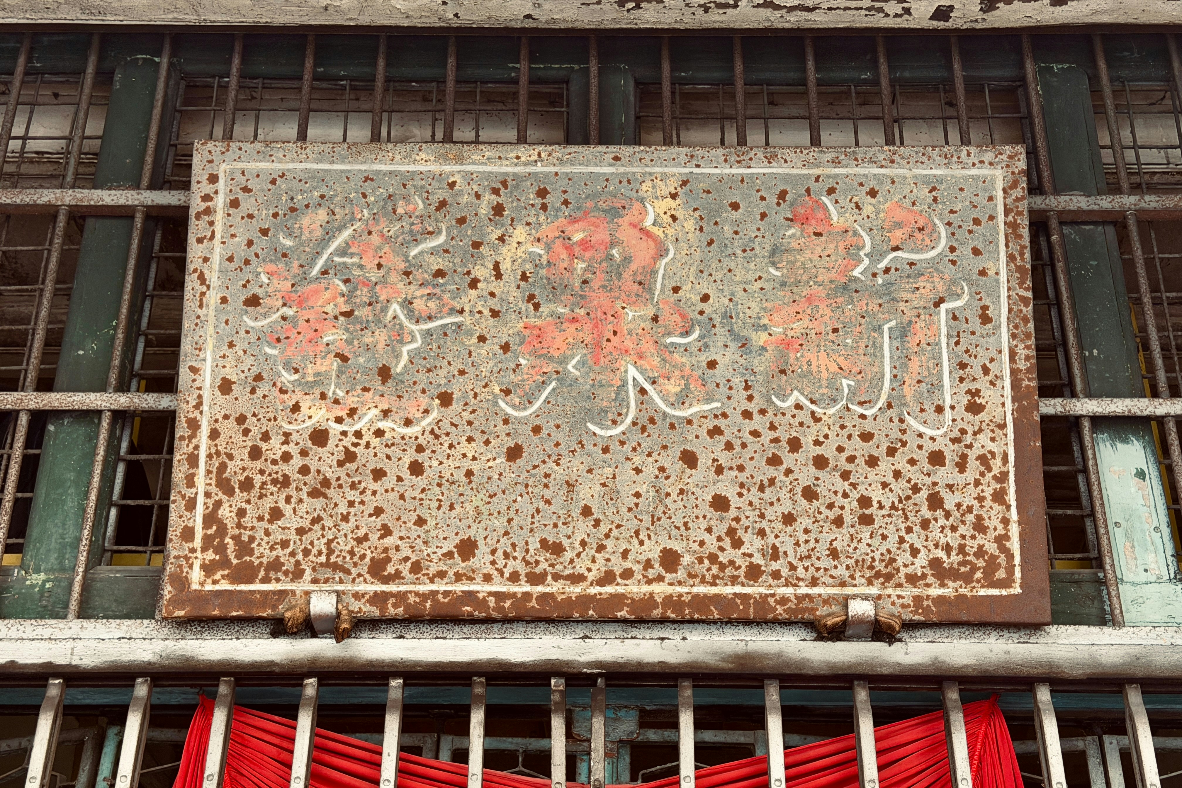 Rusted Plaque with Faded Chalked Script Above Red Drapery