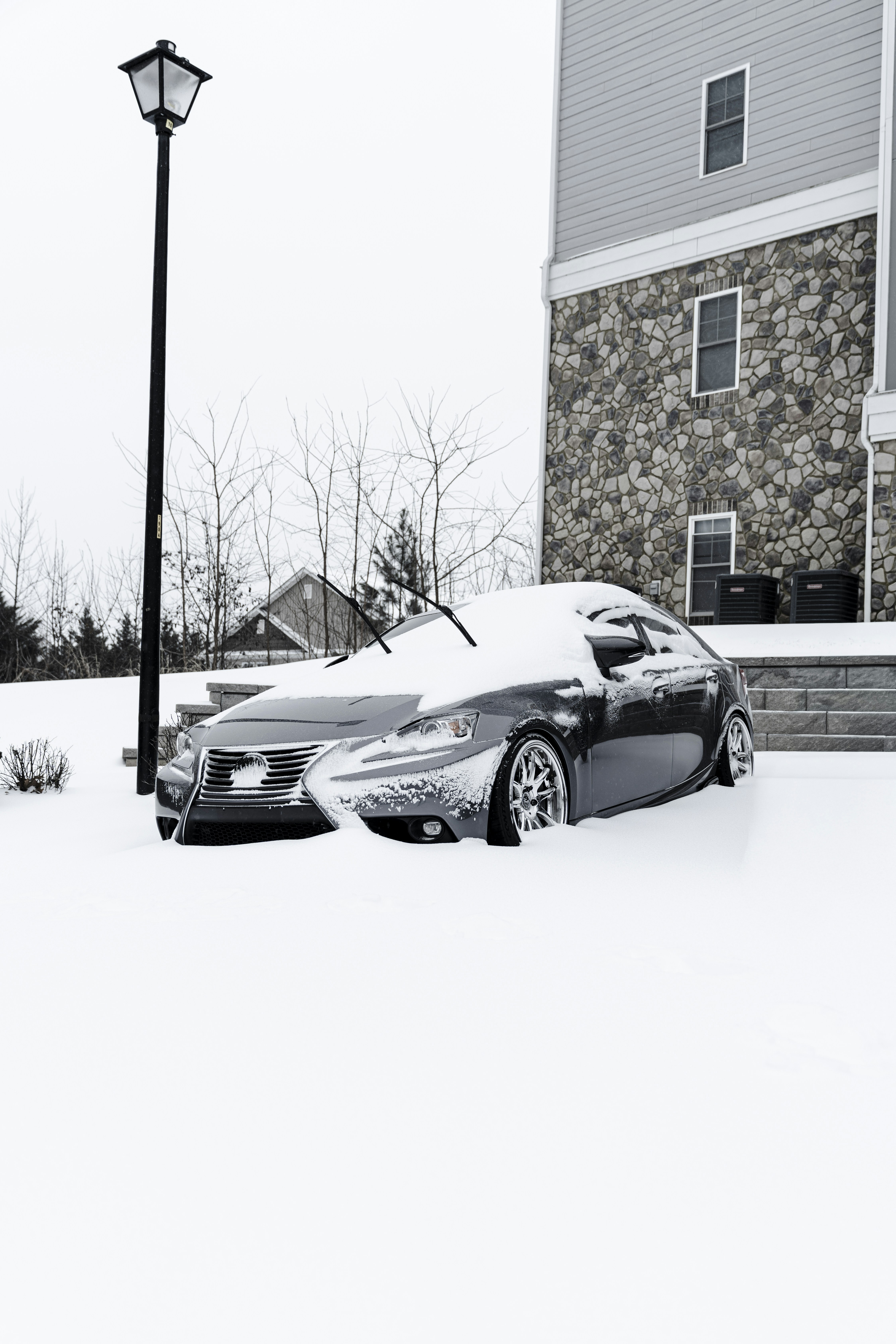 Snowbound Lexus: A car tucked beside a stone-faced residence under a streetlamp