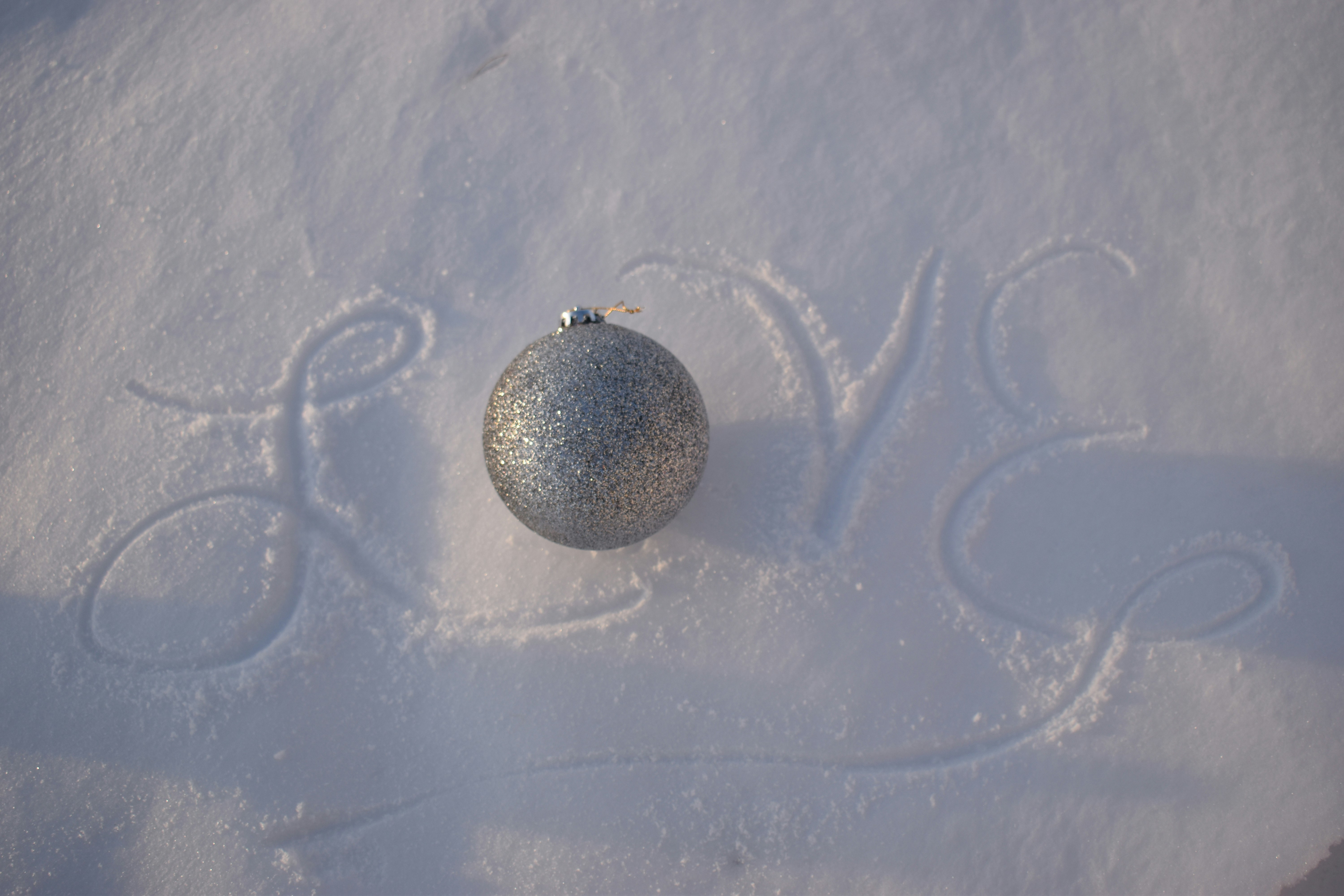 Glittering Christmas Ornament Resting on Snow with Subtle Shadow Script