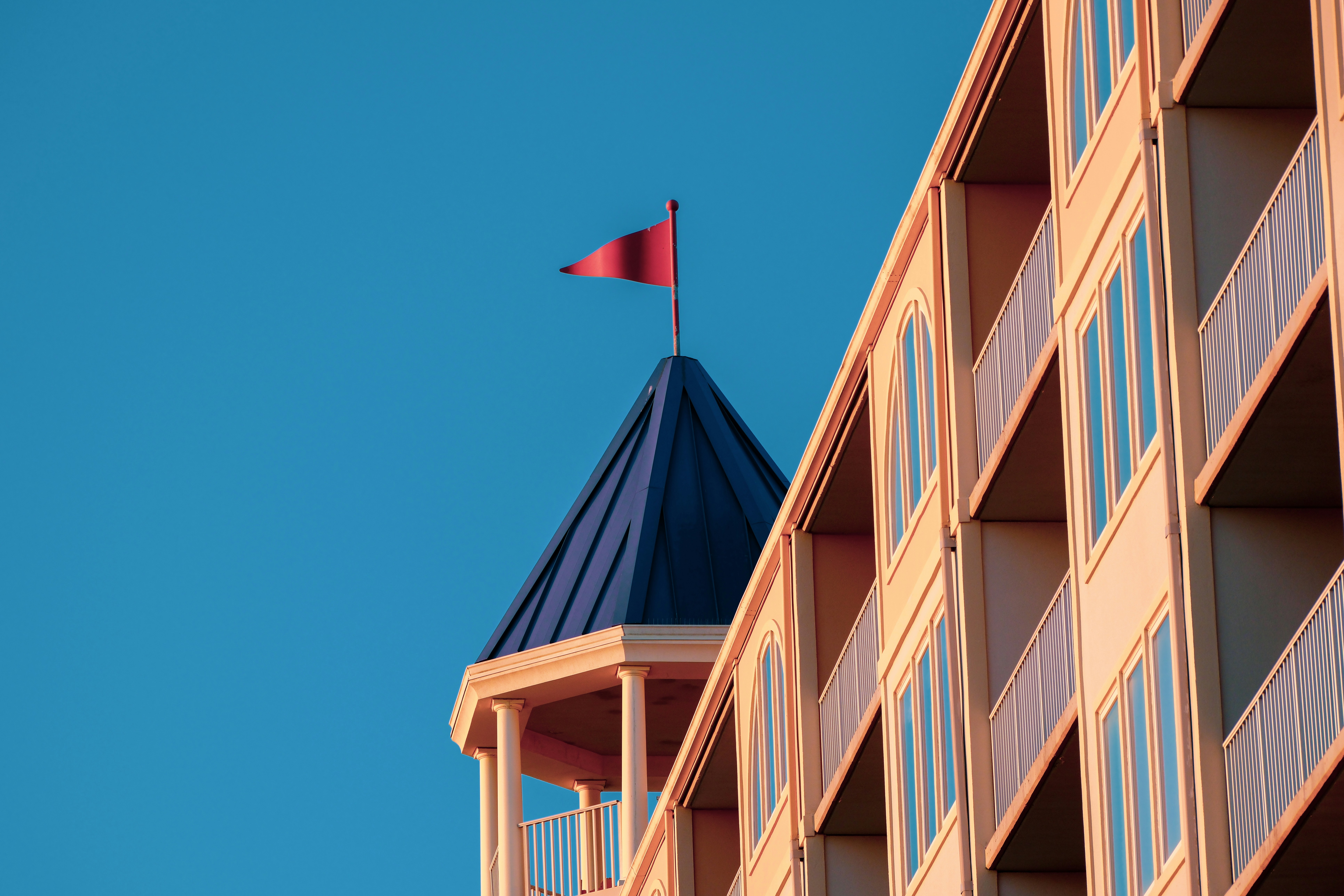 Crimson flag atop a blue-domed lookout against a sunlit modern facade