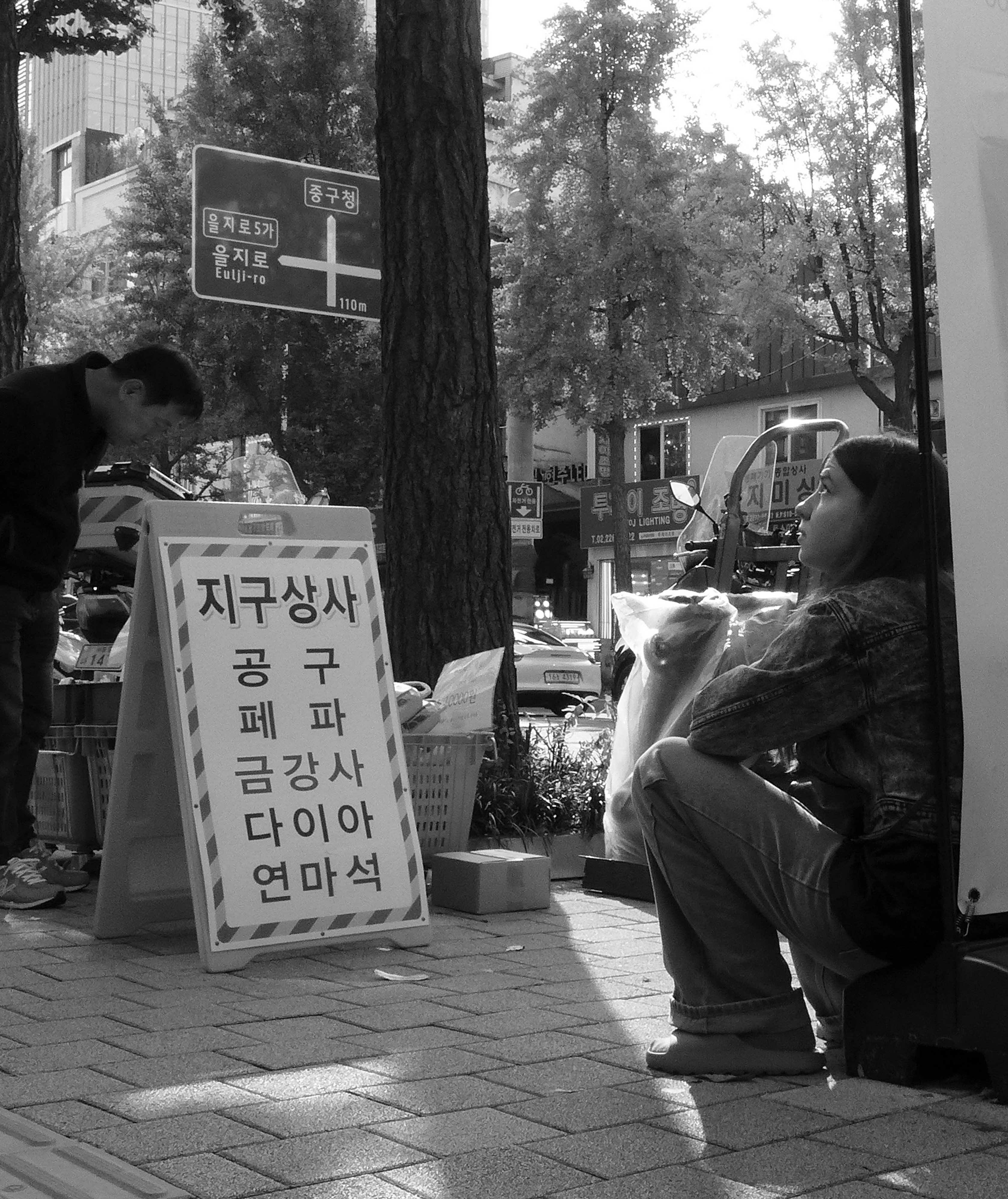 Man sitting on sidewalk near korean sign