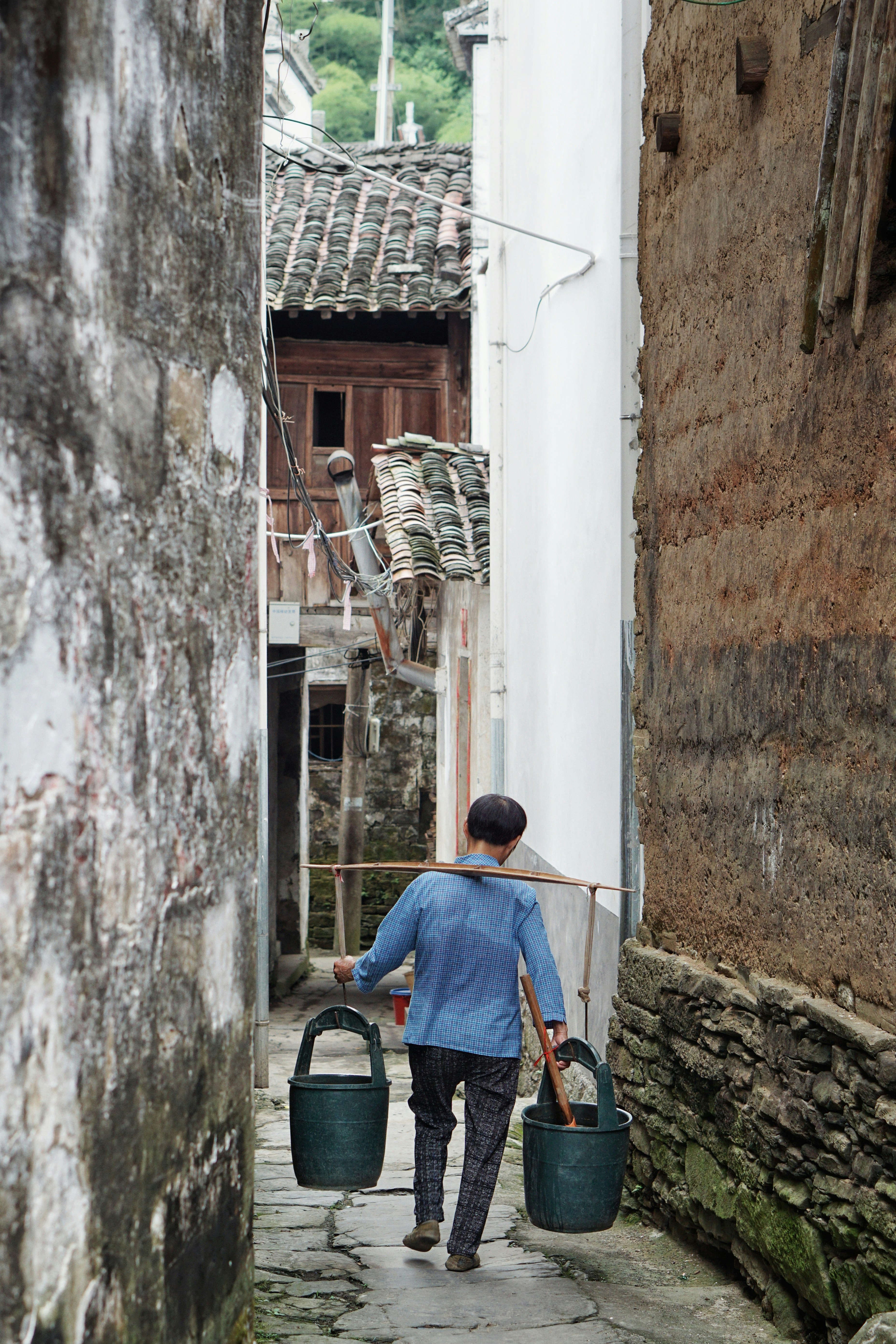 Carrier of Quiet Traditions Through a Narrow Alley