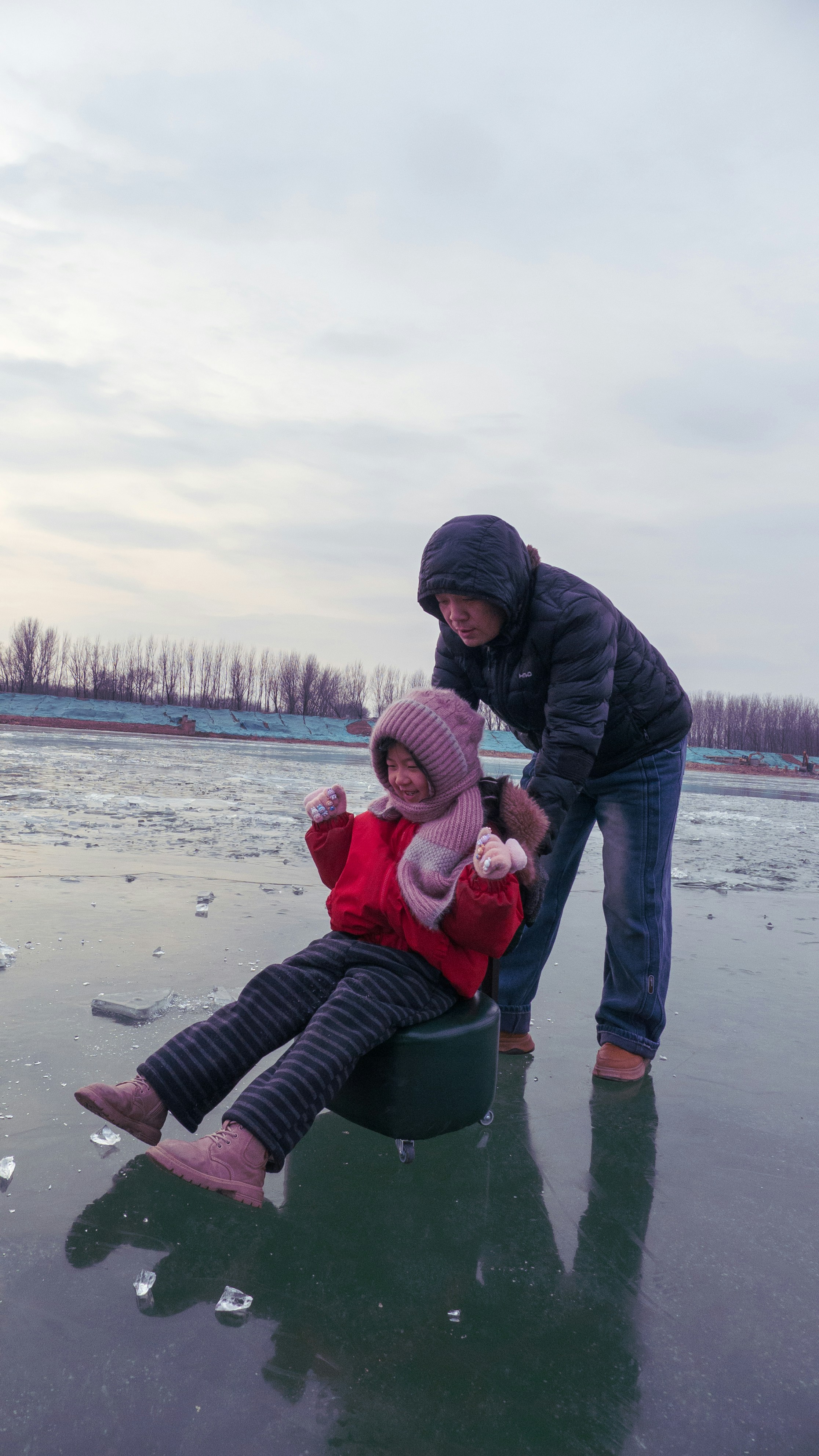 Adult pushing child on a sled on icy surface