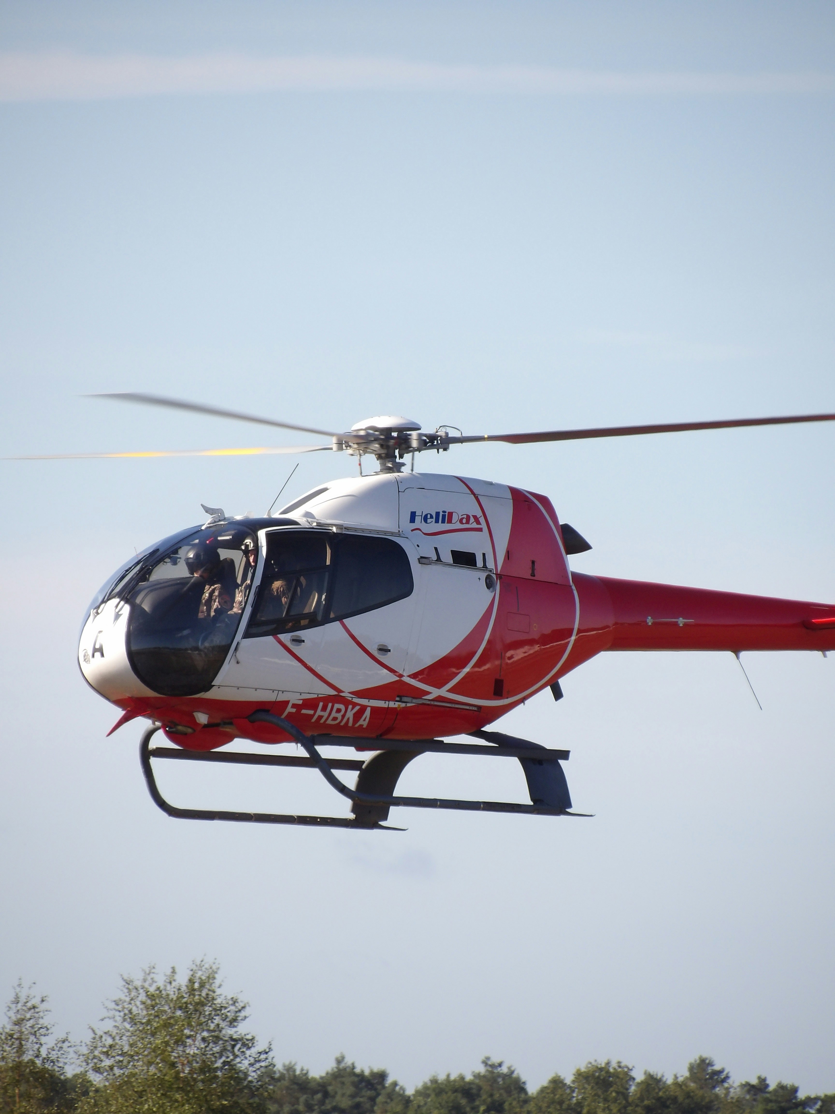 Red and white helicopter in flight against a blue sky.