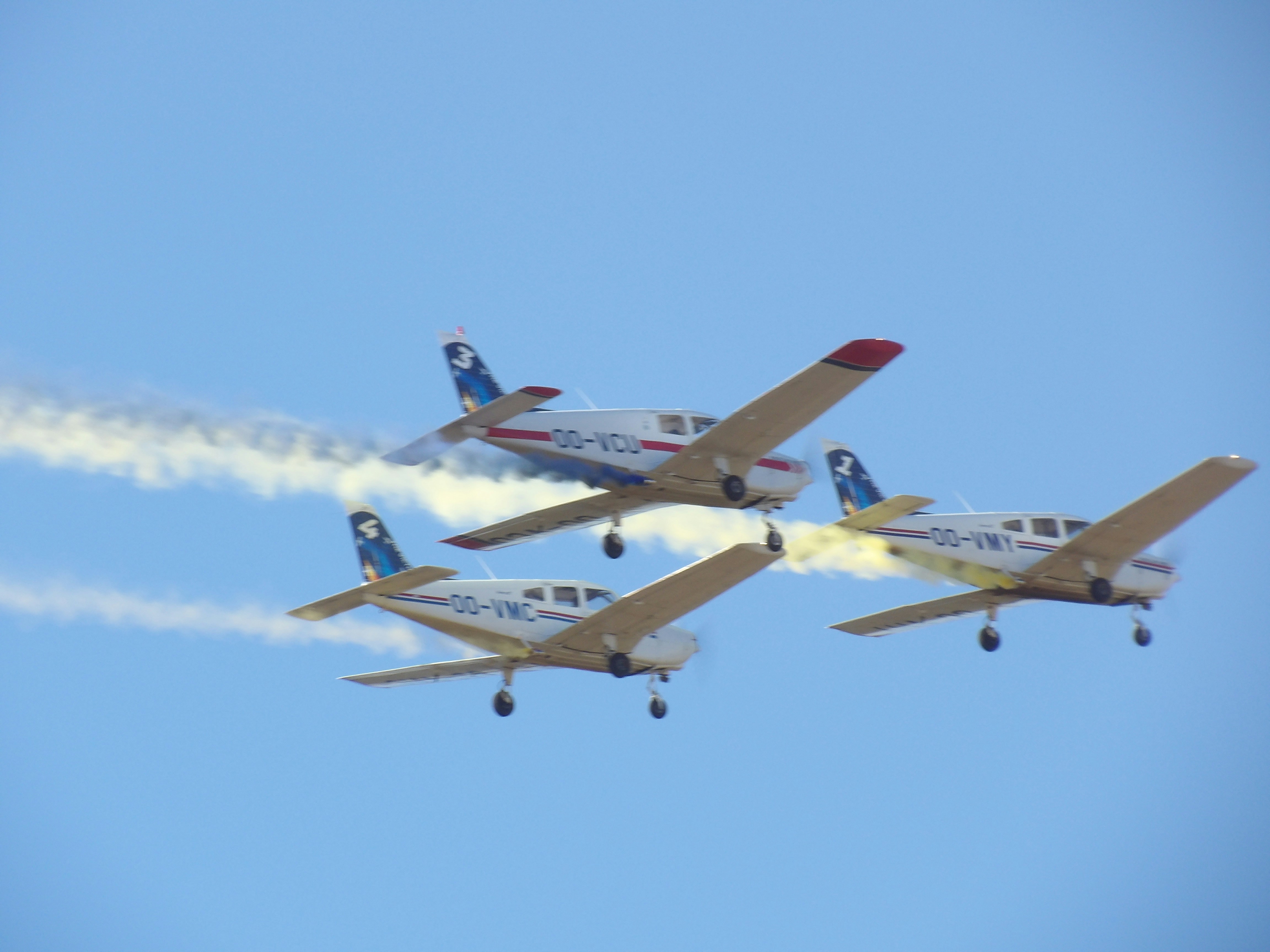 Three small planes flying in formation with smoke trails.