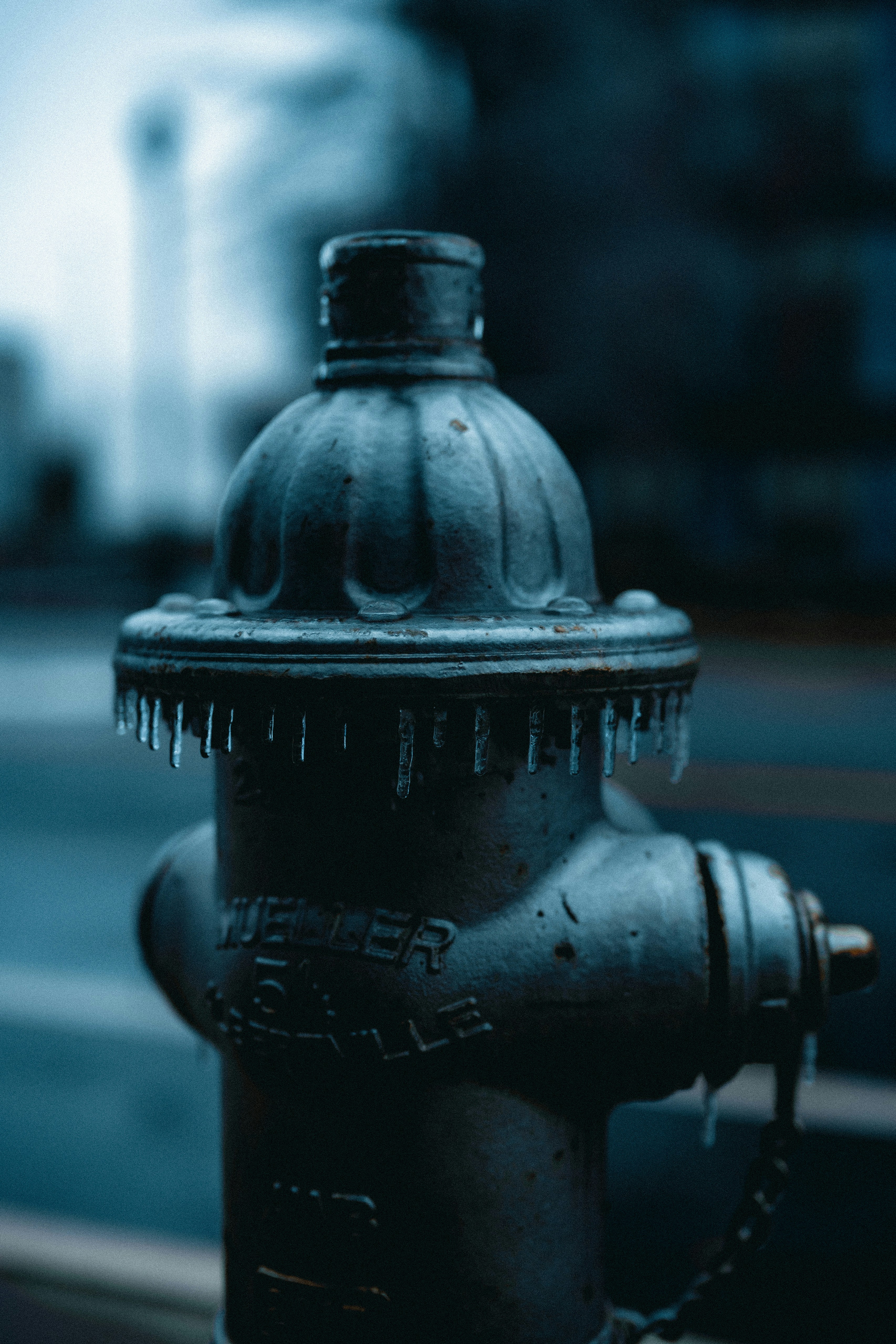 Cold Blue Quiet: A Fire Hydrant in Focus Against a Blurred Cityscape