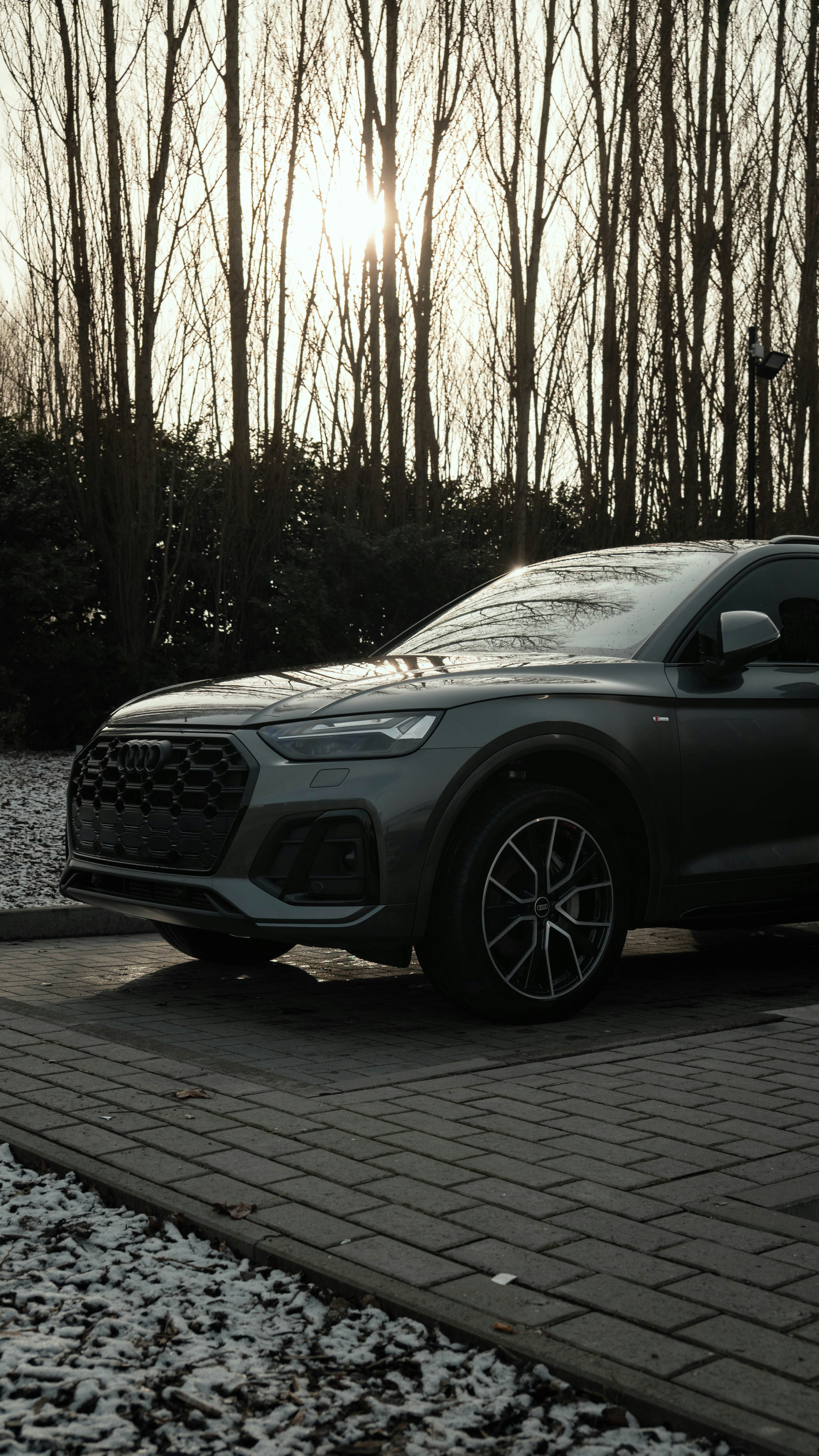 Sunlit edge: a gray Audi SUV parked along a wintry riverside road