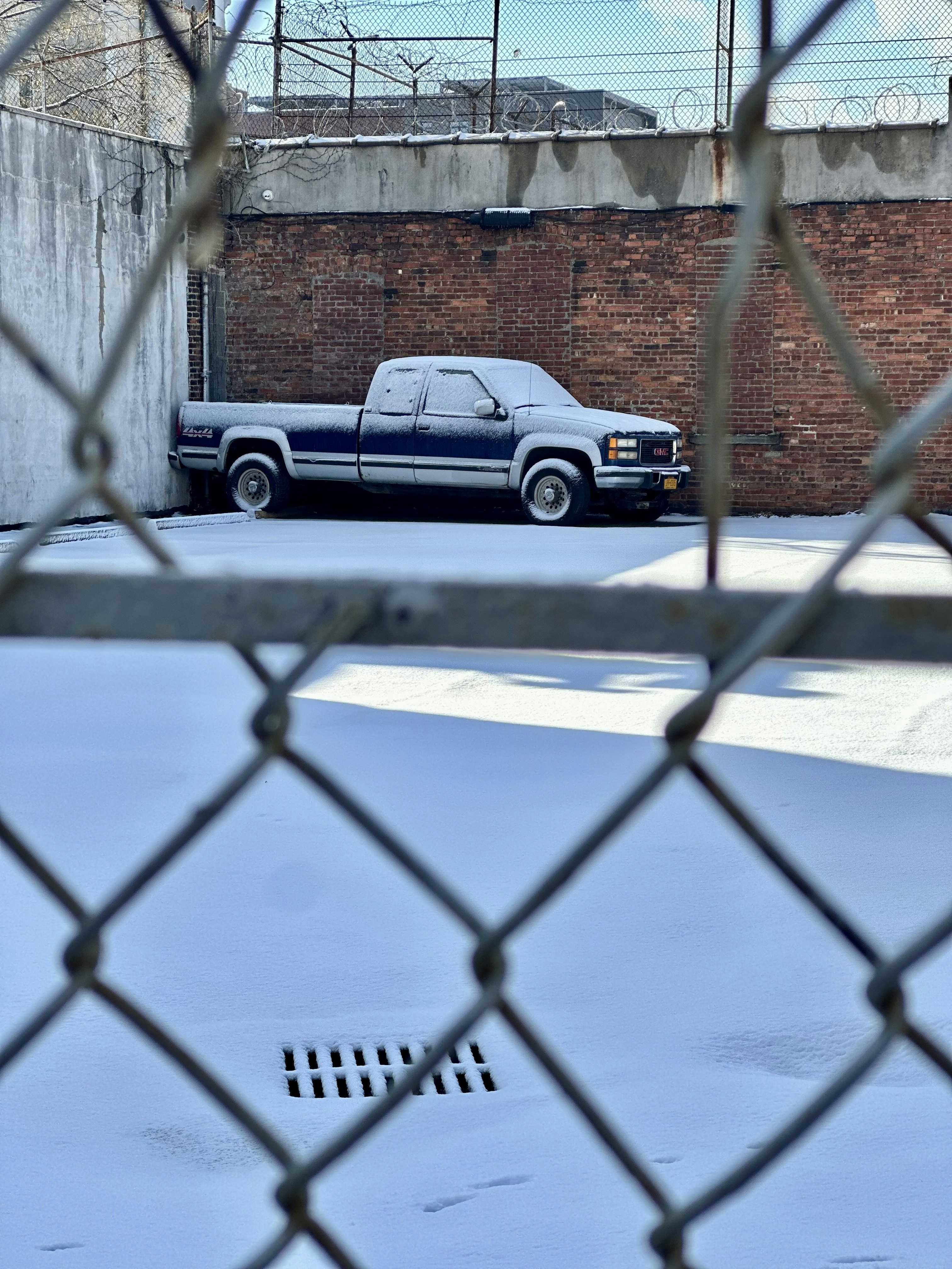 Winter Timeout: Old Chevy Resting Behind Chain-Link Shadows