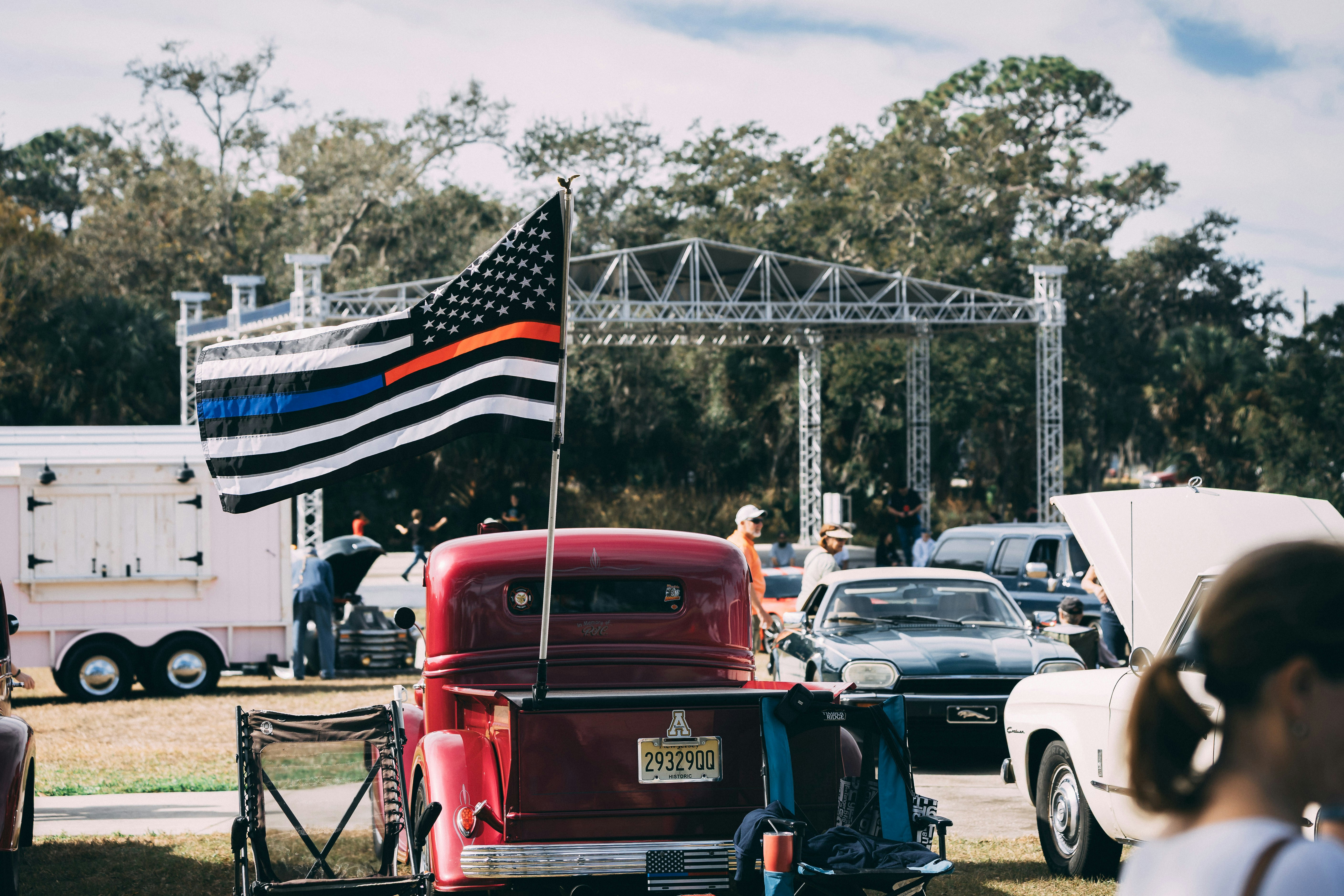 Flag and vintage car at a sunlit outdoor gathering