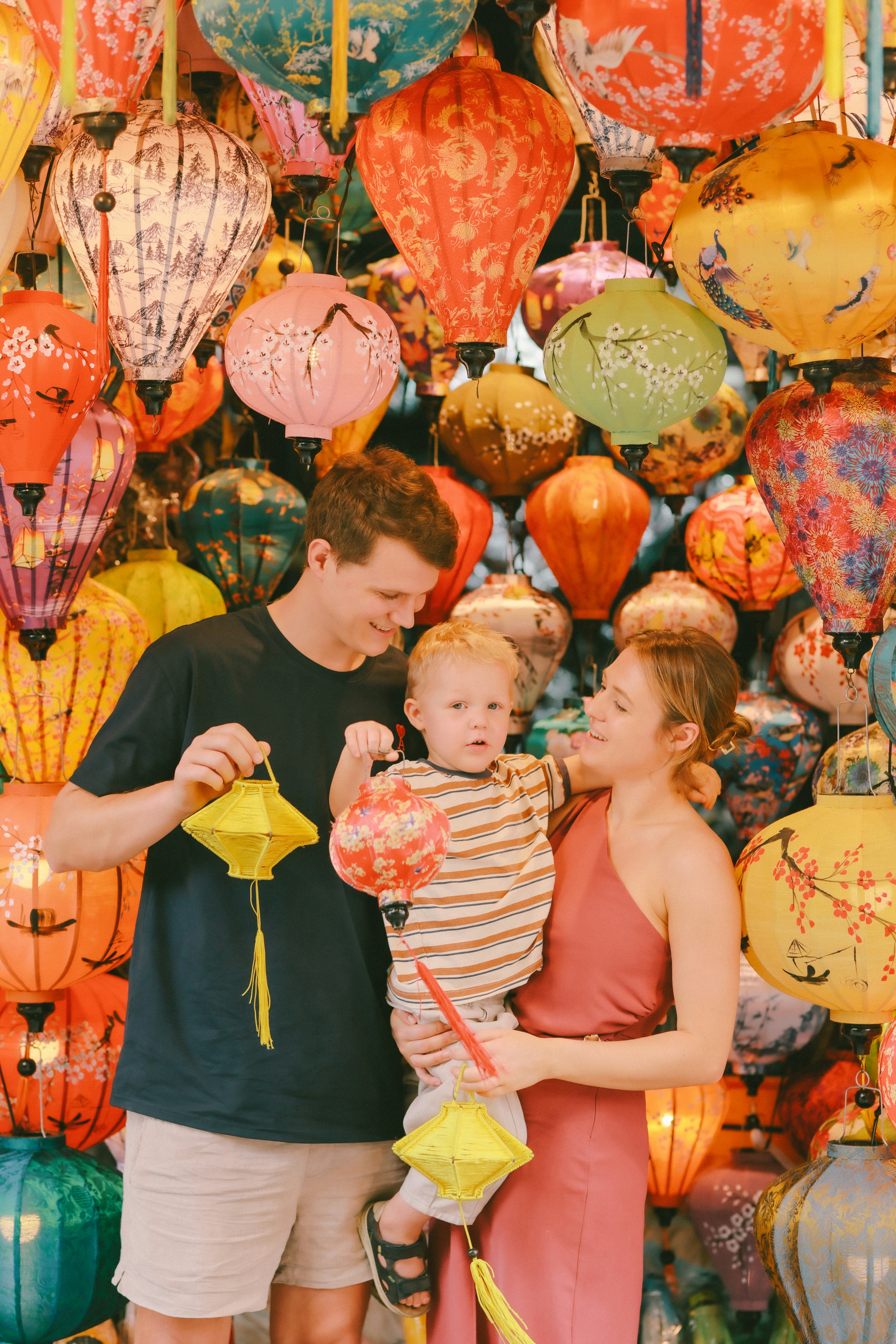 Lantern Festival Family Moment: A Father Lifts a Lantern as the Mother Holds Their Little Child Amid Colorful Orbs