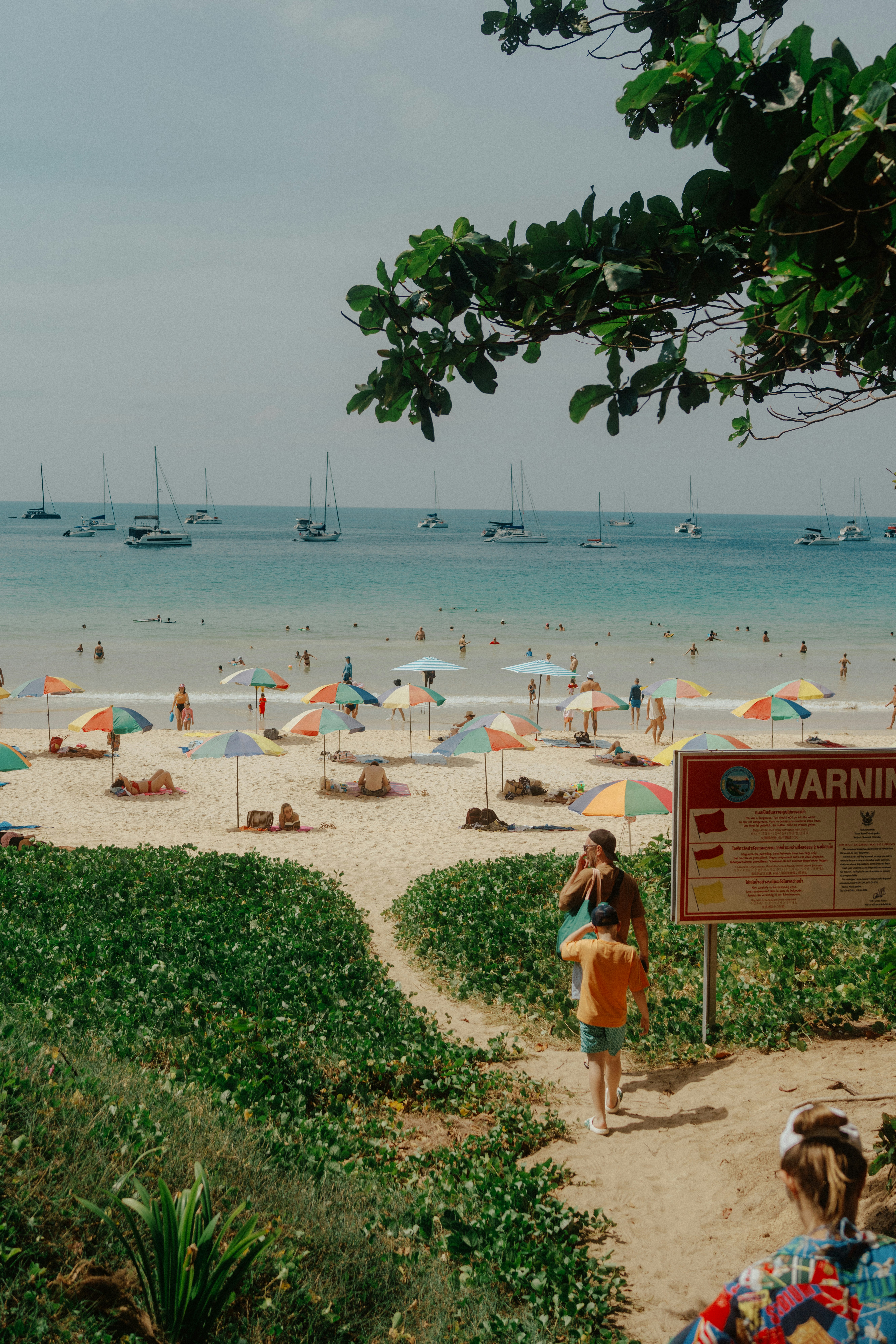 Sunlit Shoreline: Beachgoers, Umbrellas, and a Warning Sign
