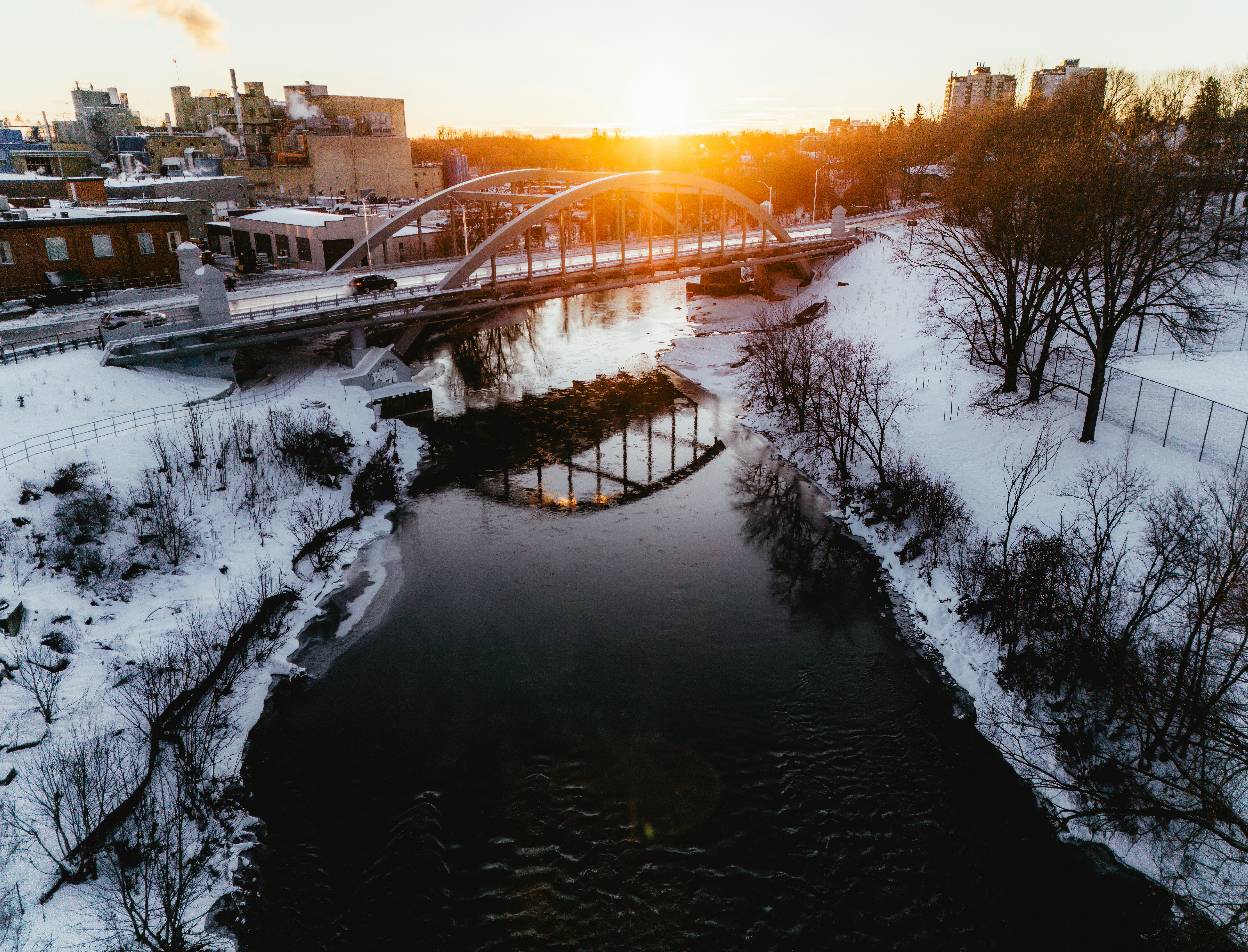 Winter Sunset Over a Snow-Blanketed River with a Pedestrian Bridge