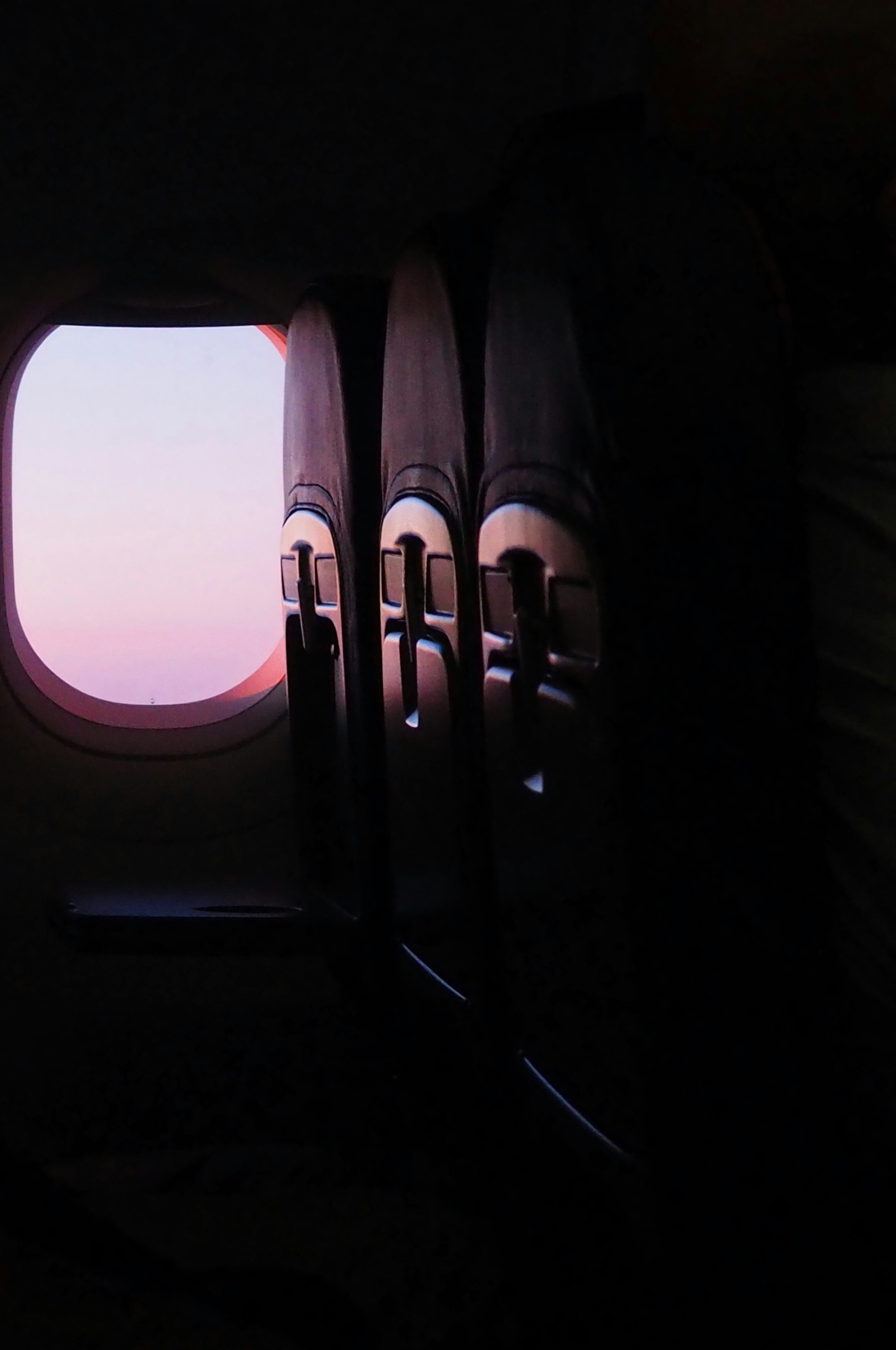 Row of airplane seats silhouetted by the window at sunset