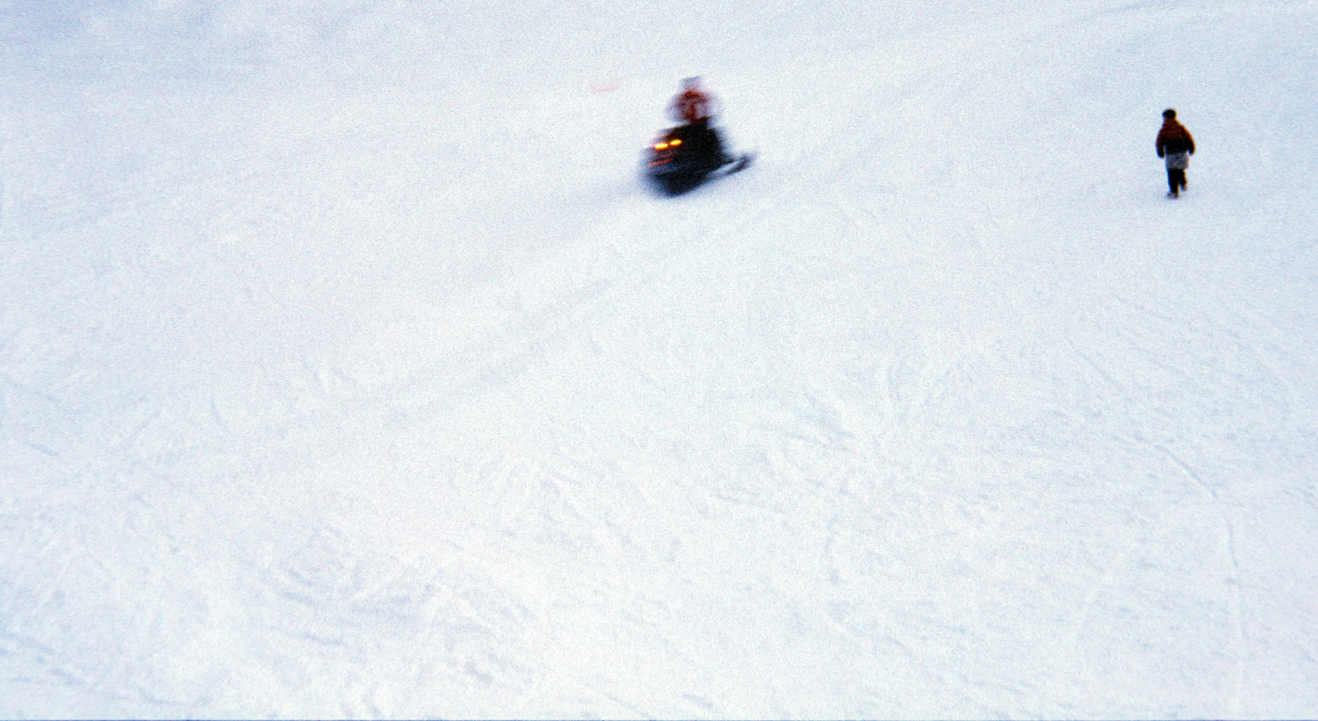Snowbound duo: a distant rider and a solitary skater drift across a quiet slope