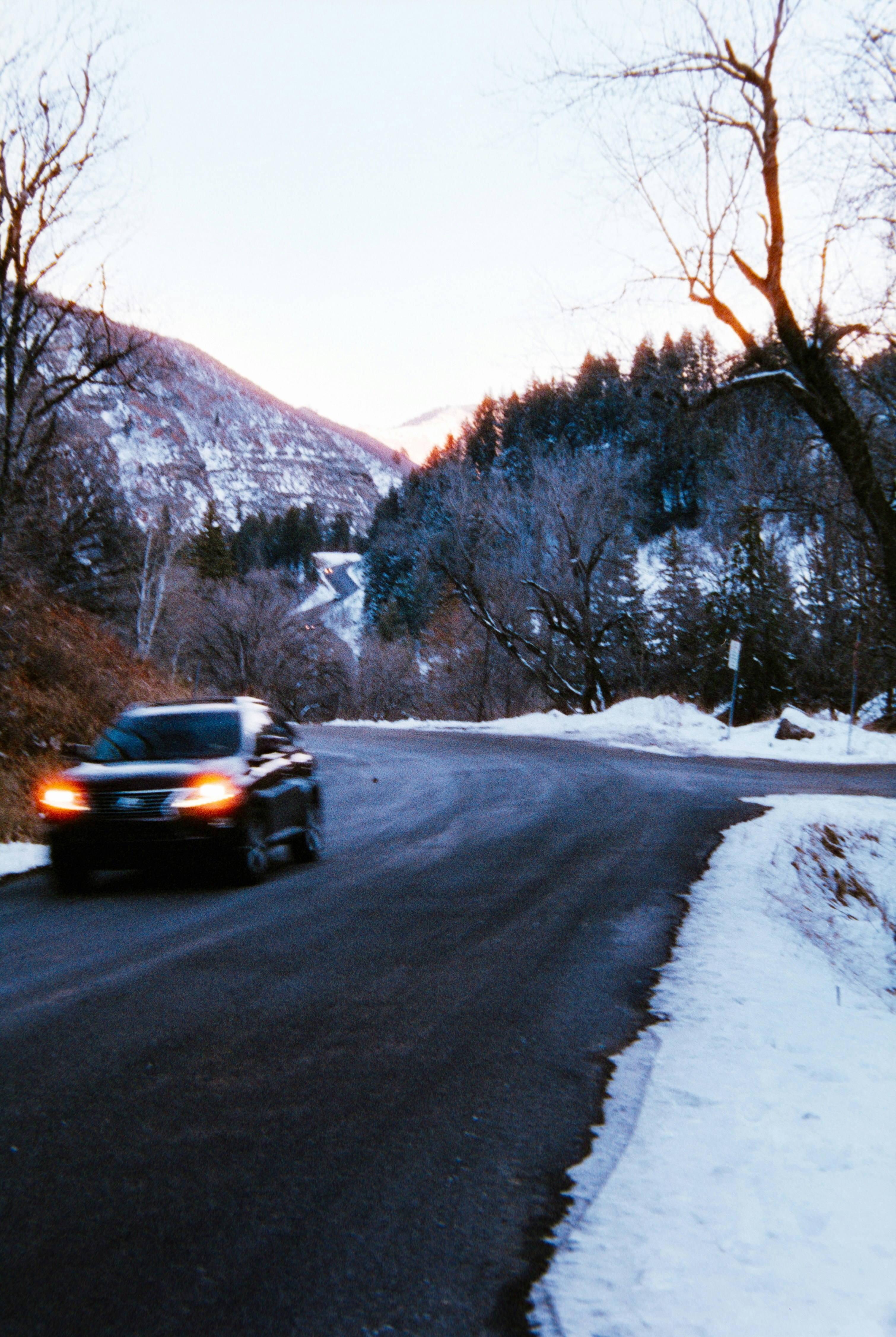 Snowy Curve: A Car Navigates a Winding Mountain Road at Dusk
