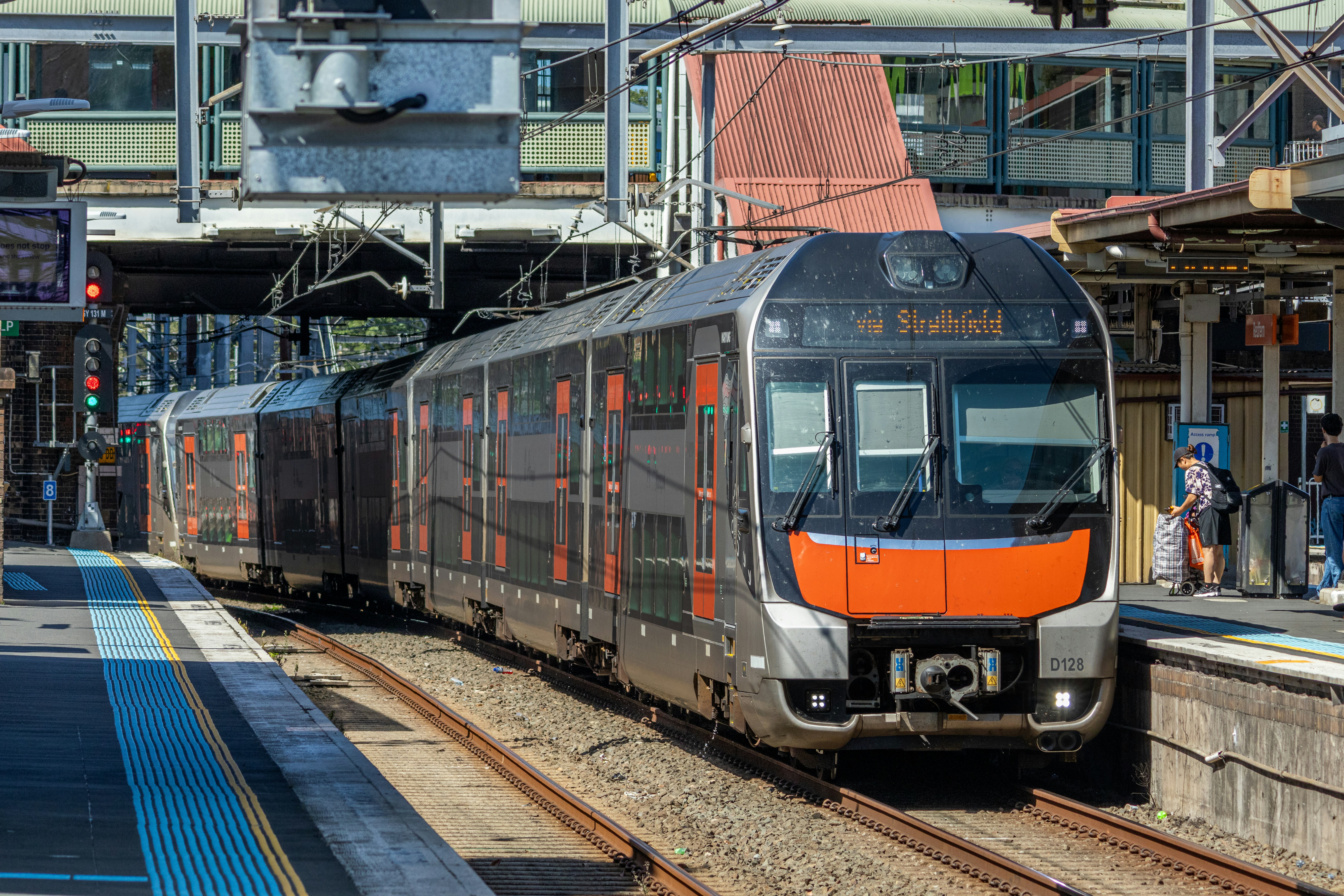 Orange-fronted train at a sunlit suburban station