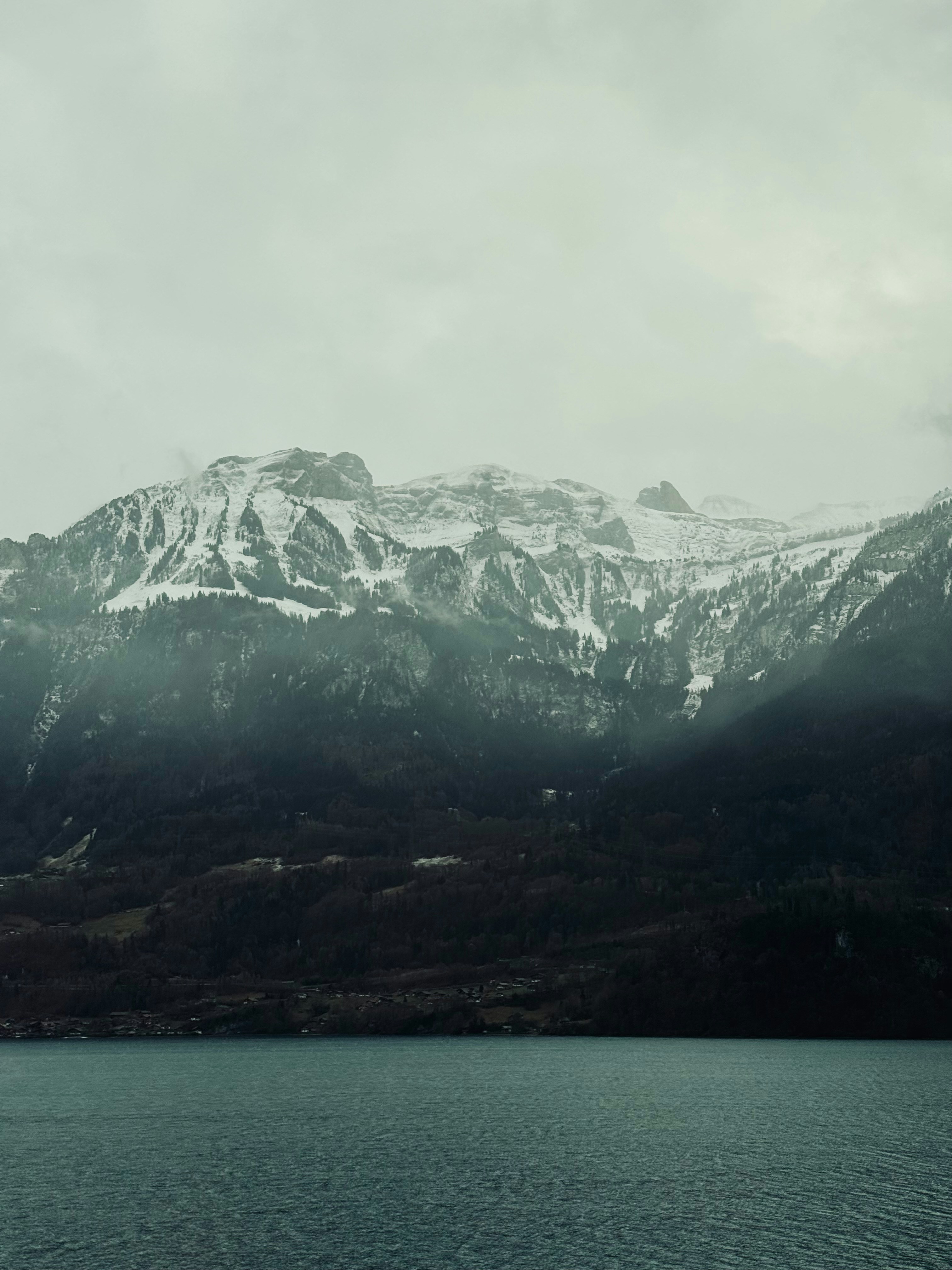 Snow-capped peaks over a tranquil lake under a pale sky