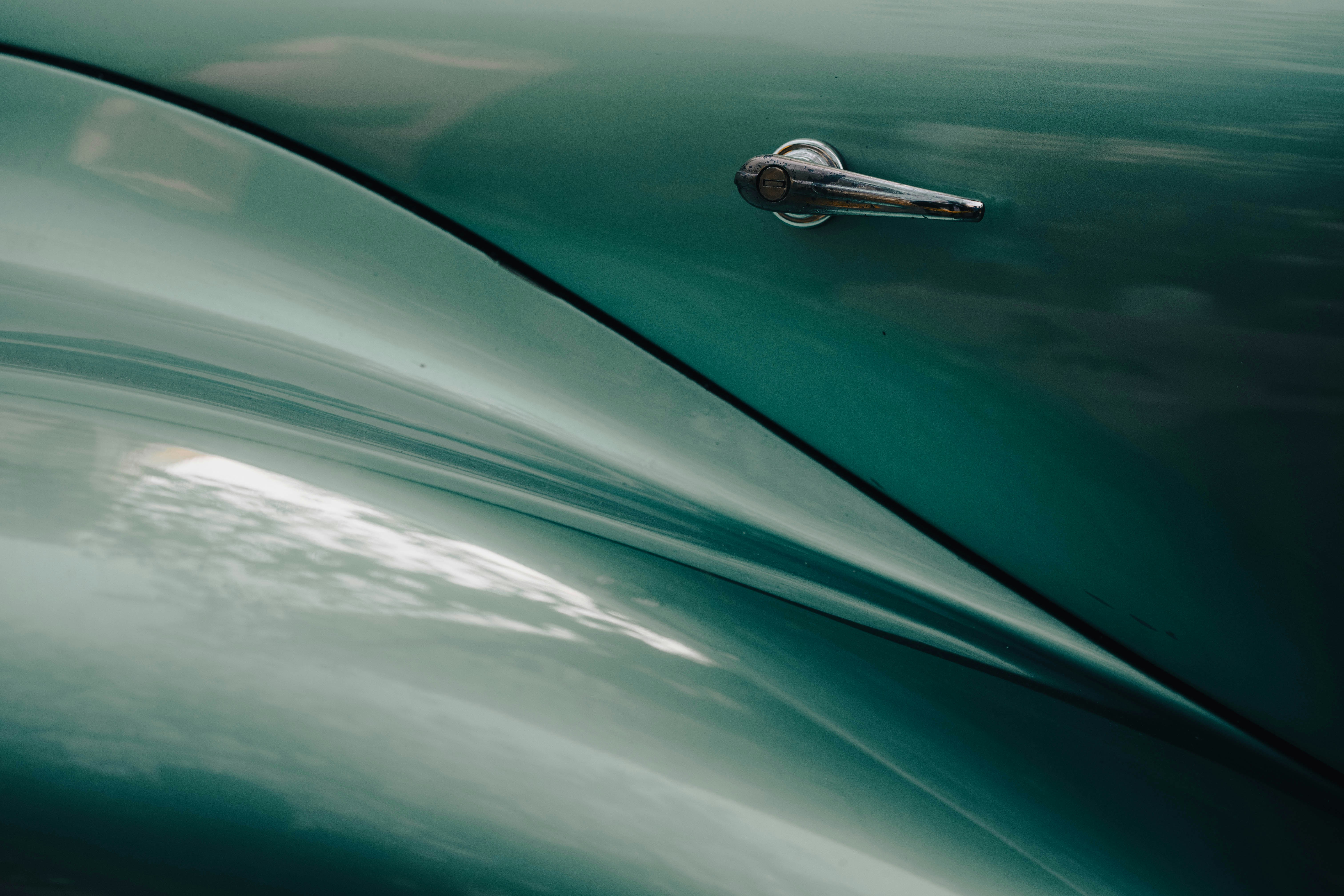 Sculpted teal curves: a classic car’s chrome badge against the flowing bodywork