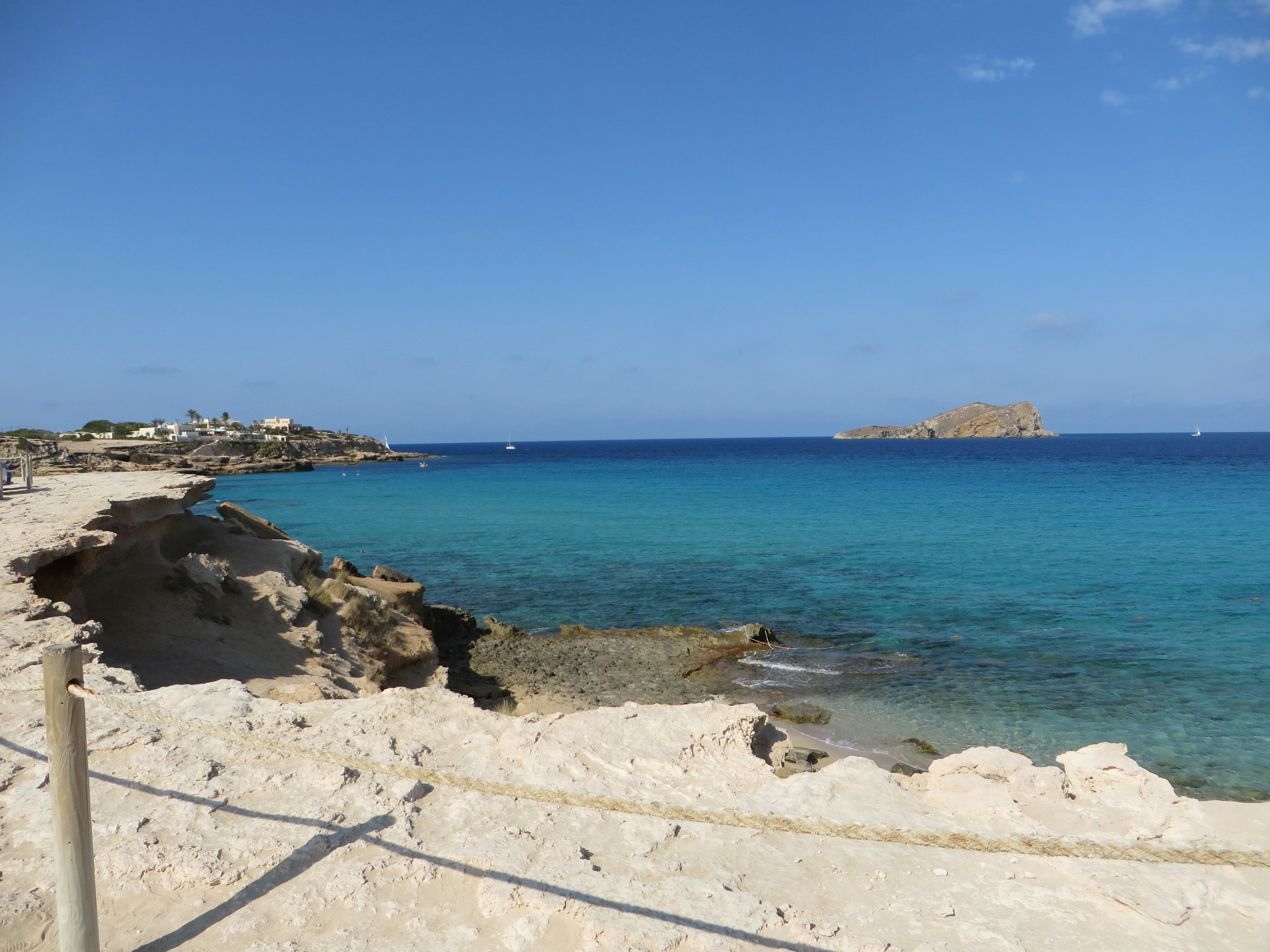 Rocky coastline with clear turquoise water and distant island.