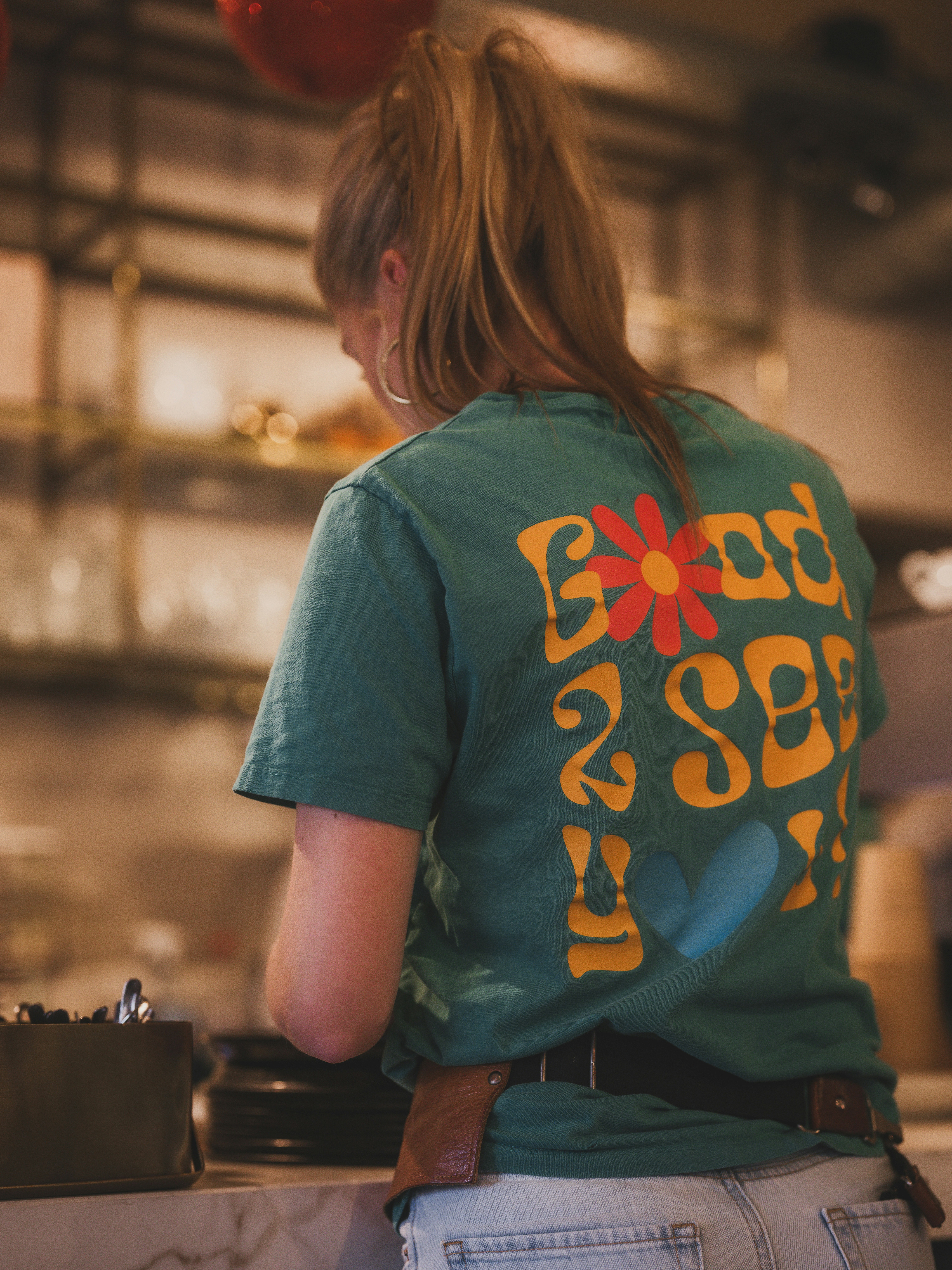 Back View of a Barista in a Teal Shirt with a Floral Graphic