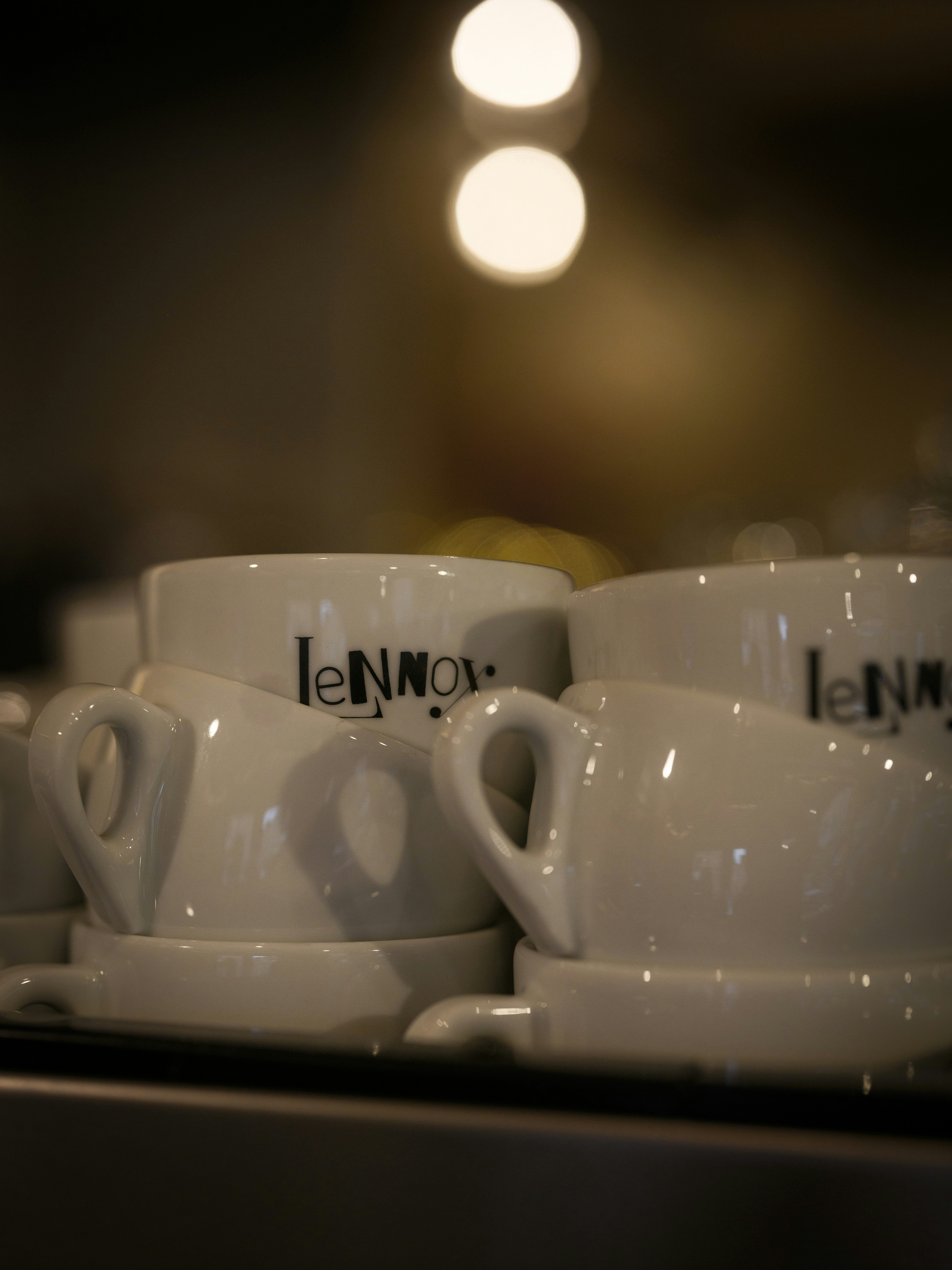 Stacked Espresso Moments: White Cups with LeNnoy Marking in Soft Bar Lighting