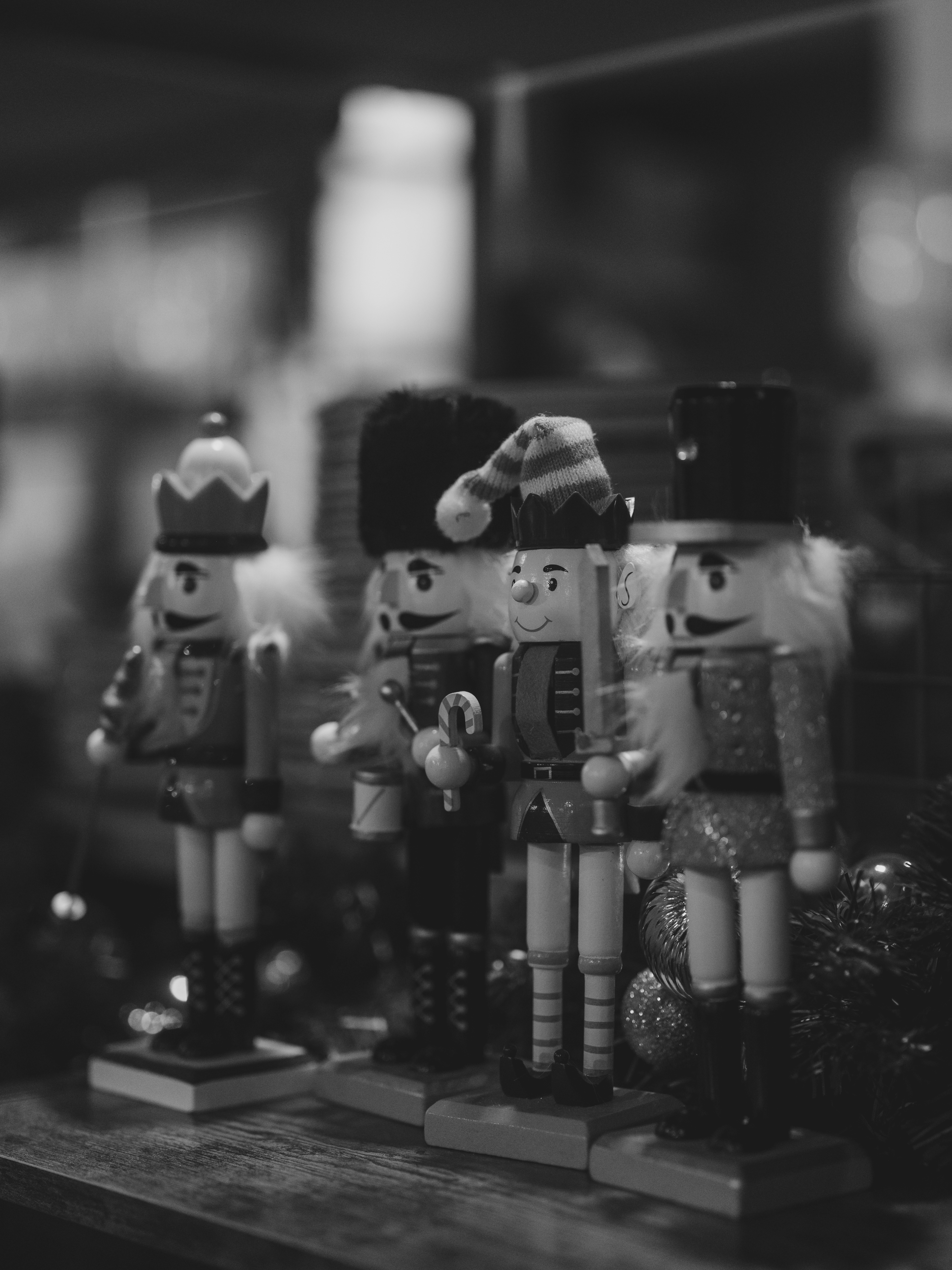 Four wooden nutcracker figures stand in a row on a wooden surface, softly blurred in a moody black-and-white scene.