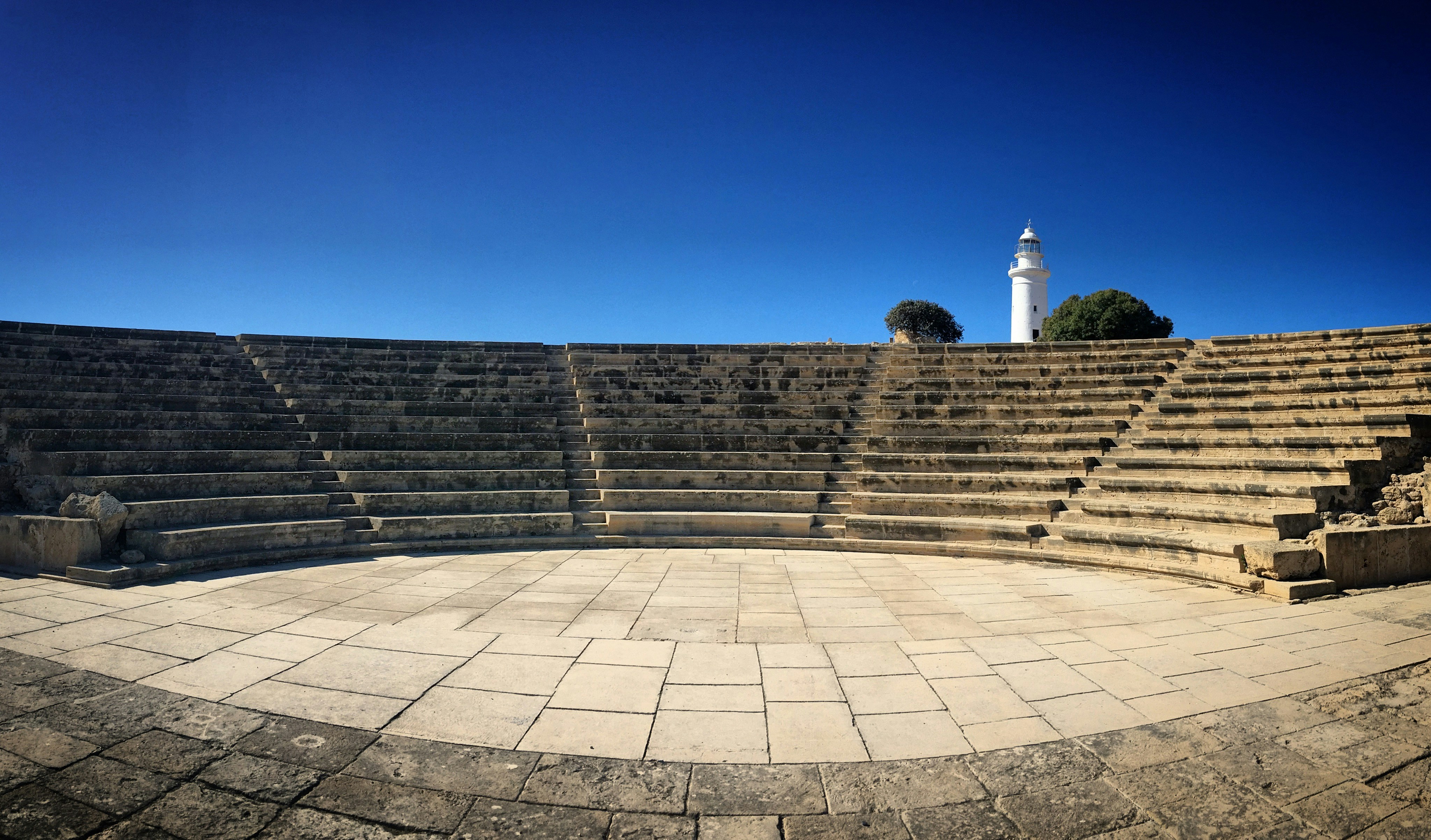 Circular amphitheater under a clear blue dome with a distant lighthouse