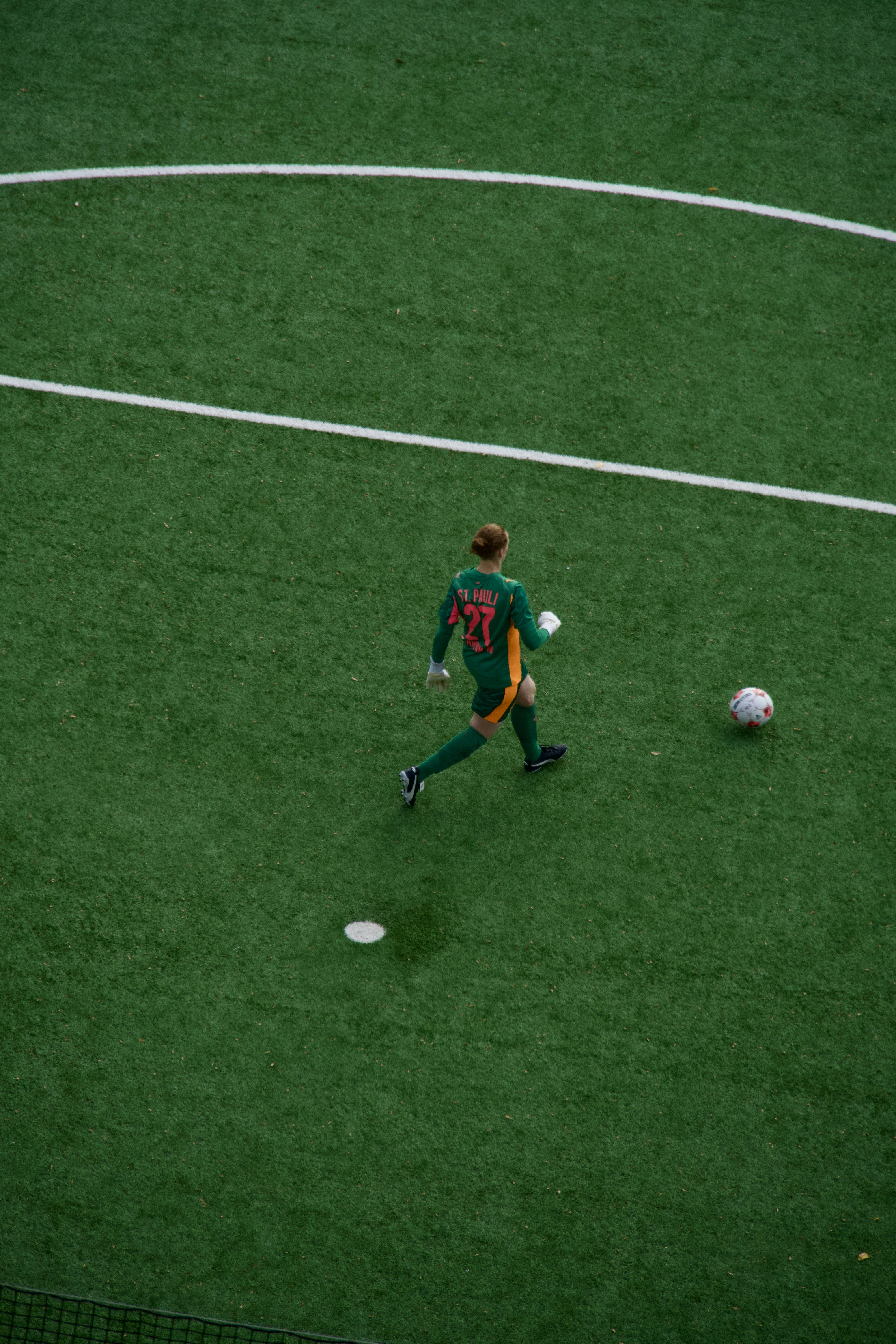 Keeper in Green: A lone soccer goalkeeper advances toward a lone ball on a lush field