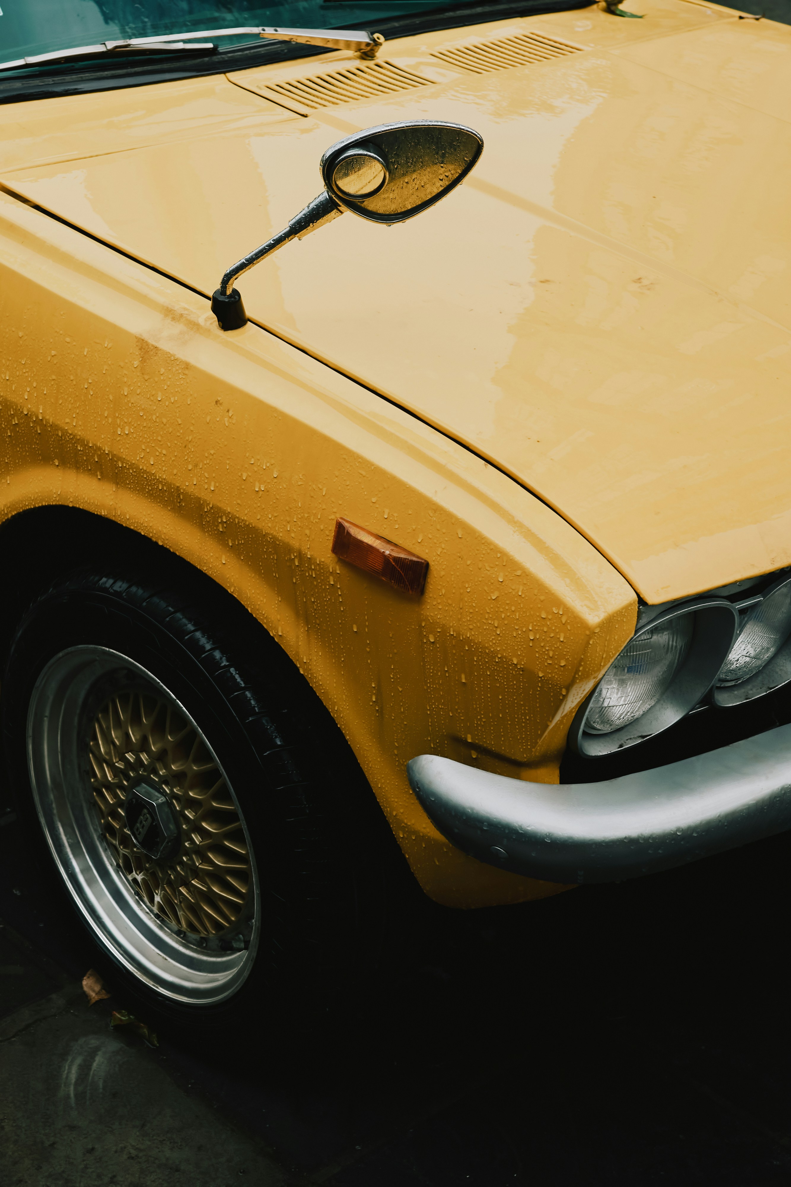 Yellow vintage car hood and mirror: a close-up rain-kissed detail