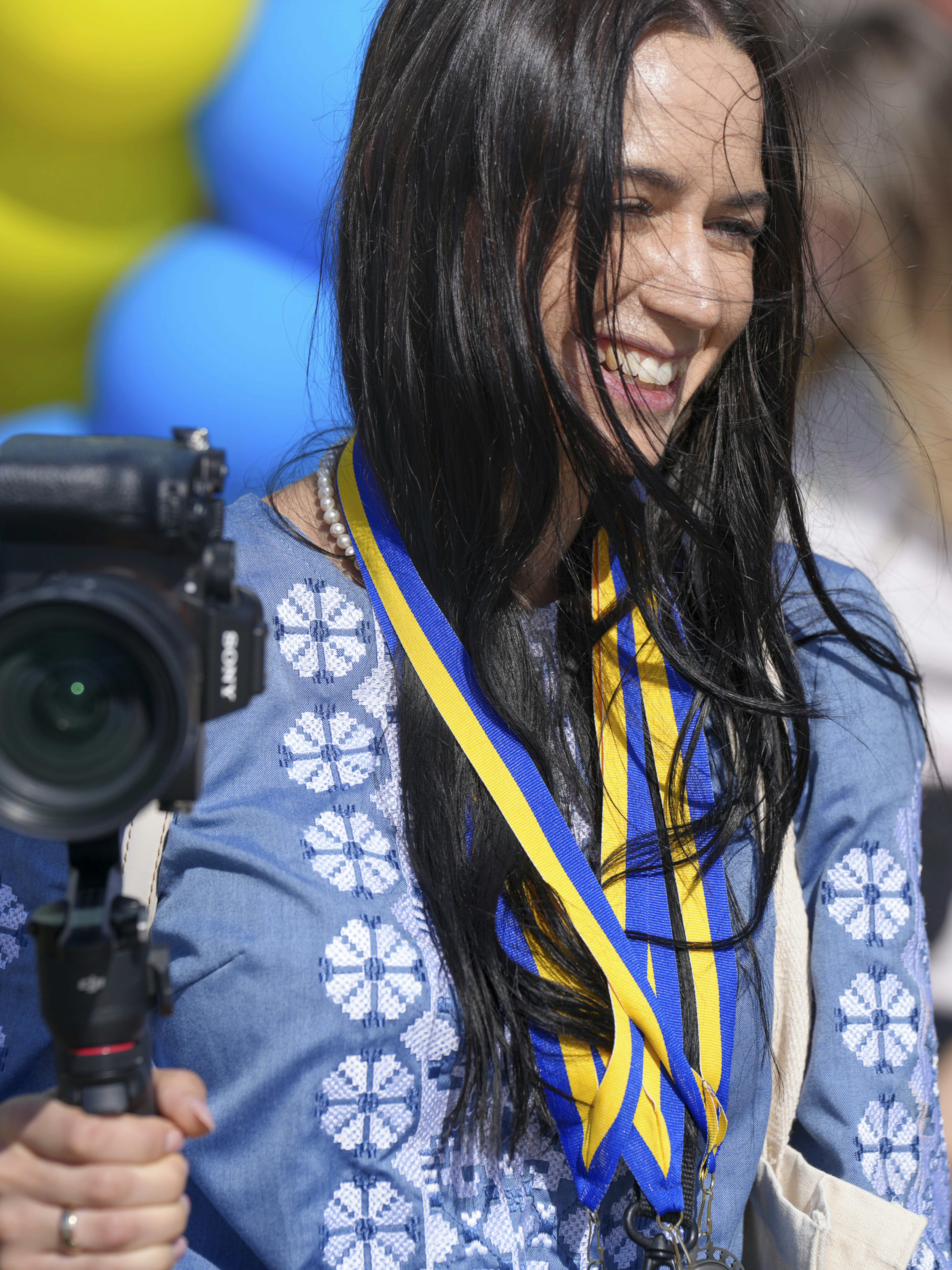 Smiling photographer with a blue embroidered dress and yellow-blue ribbons