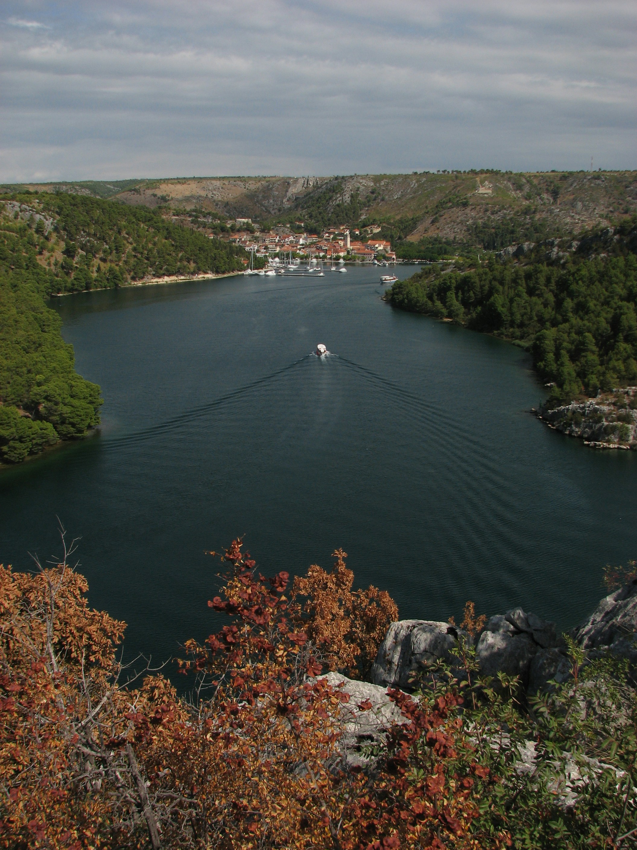 A boat travels down a wide river towards a town.