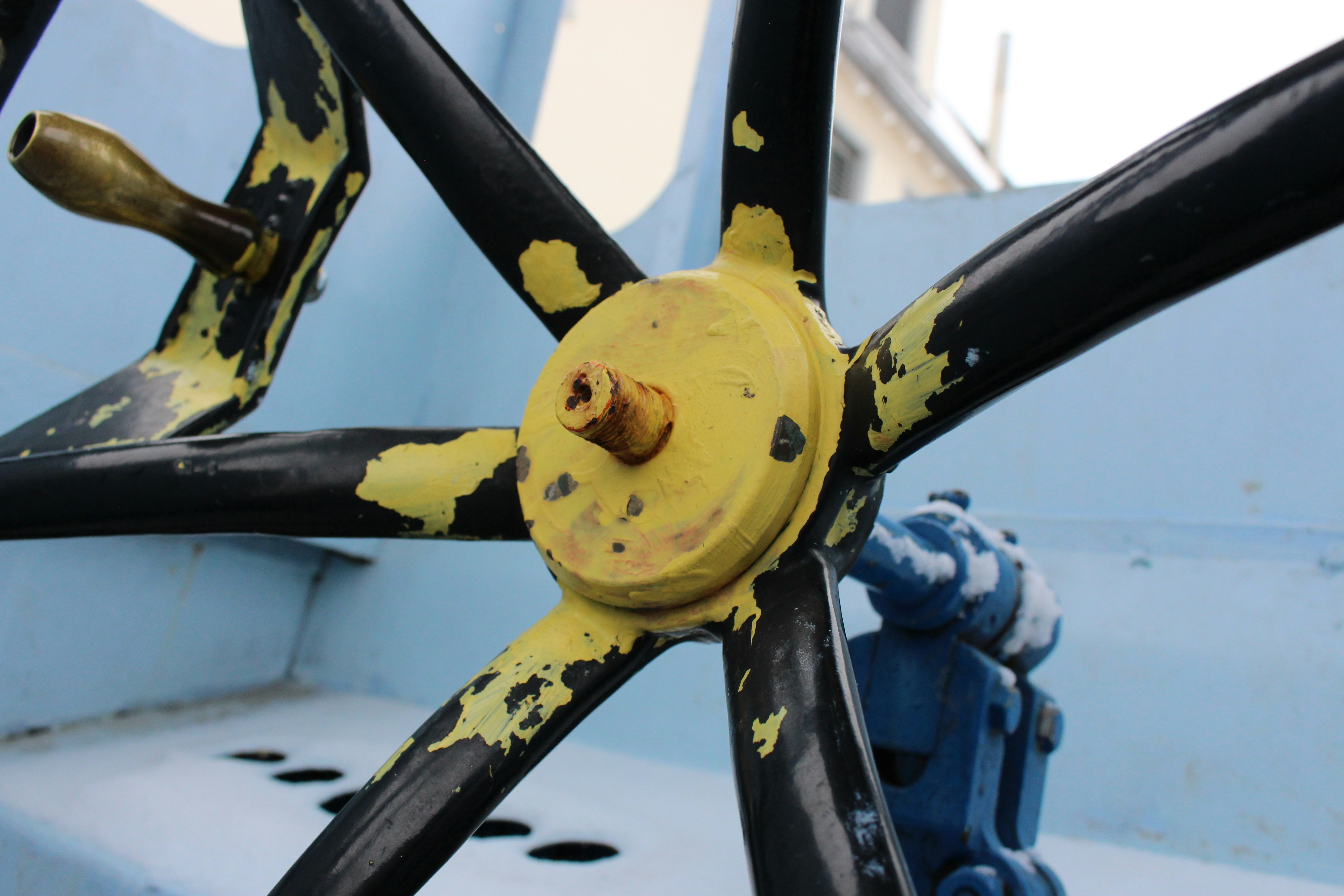 Weathered helm: close-up of a yellow hub amid black spokes on a pale blue deck