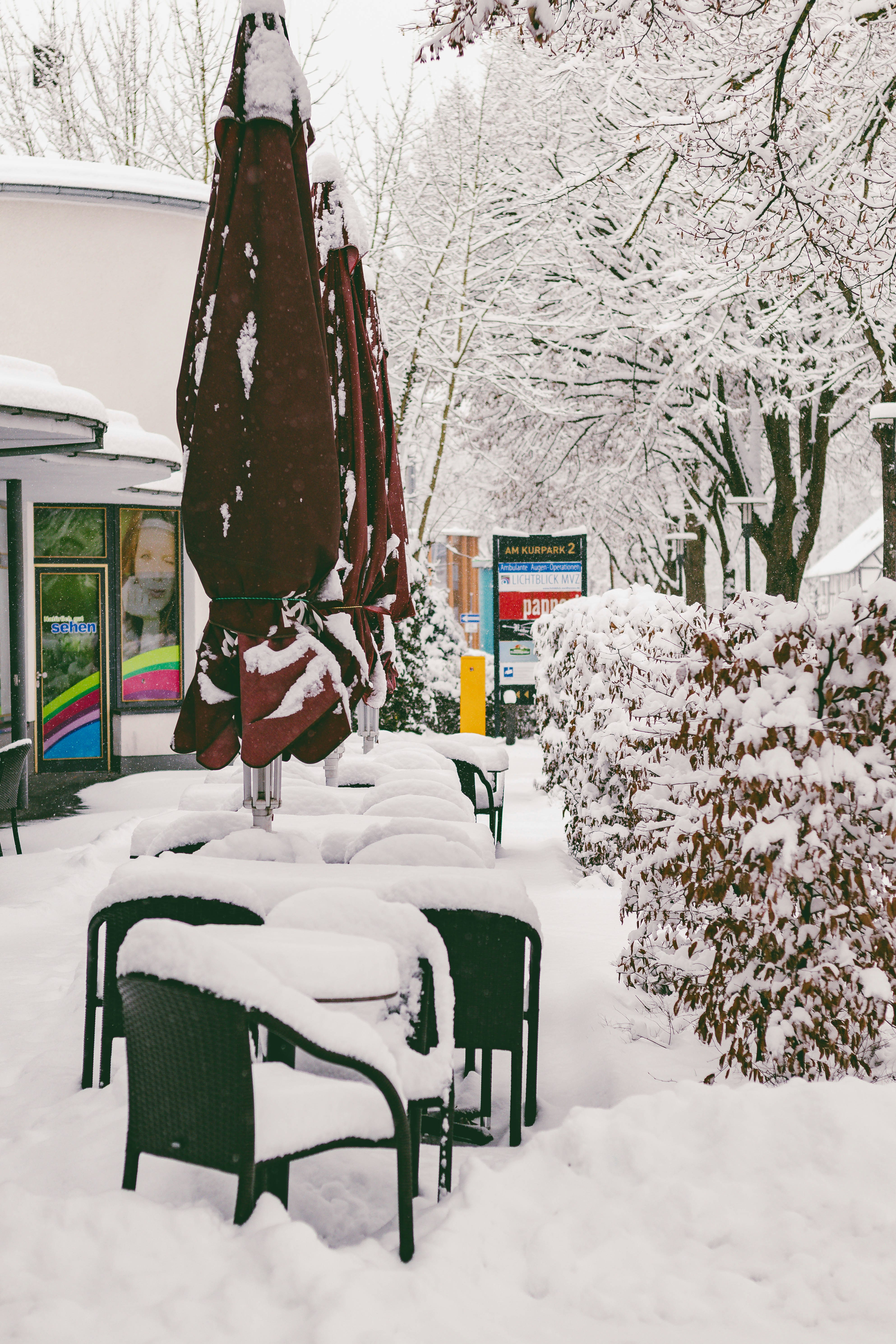 Snow‑kissed patio chairs under folded red umbrellas lining a frosted street