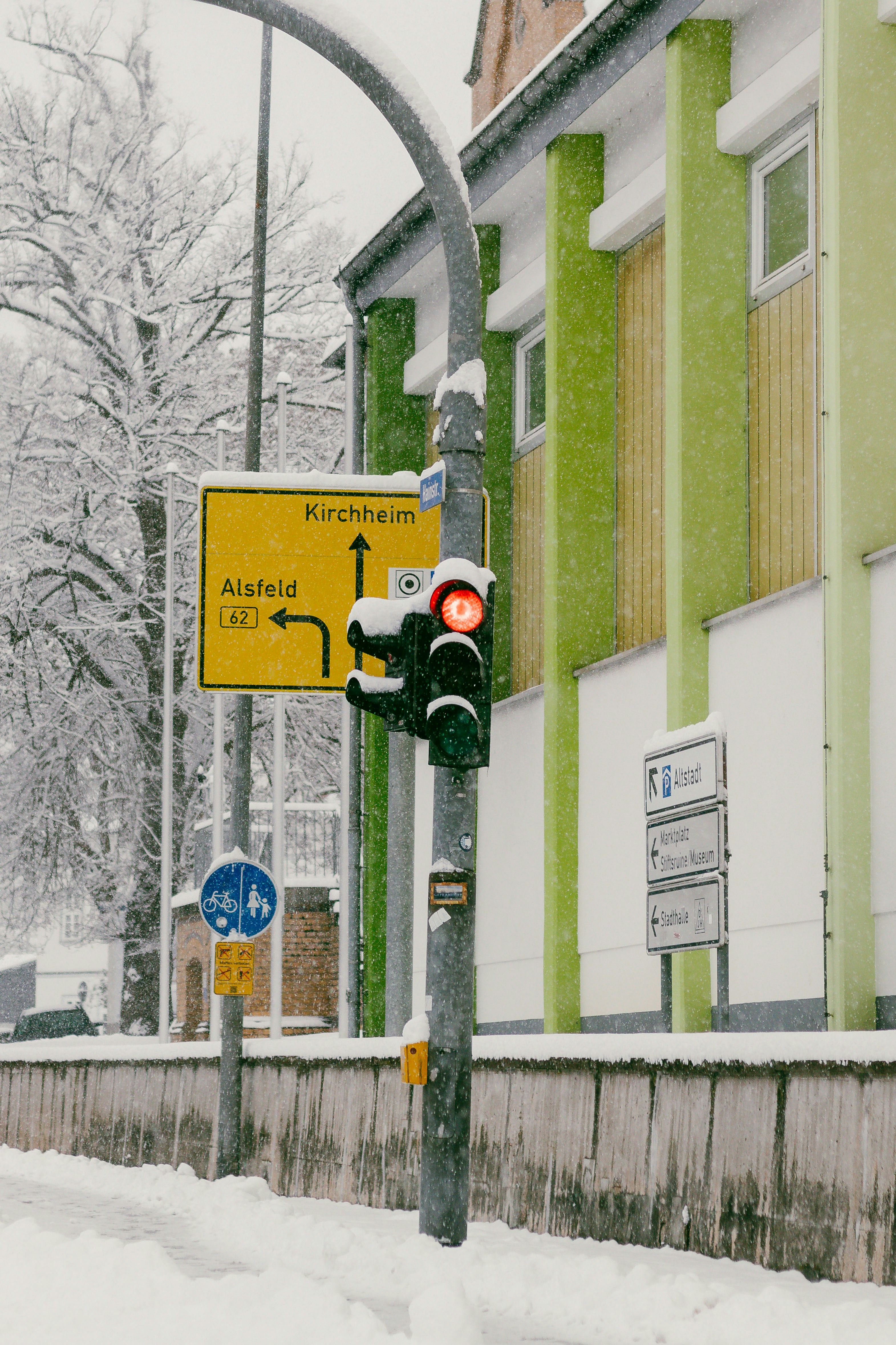 Snowy Streetlight Pause: A Red Signal Beneath Green Facades