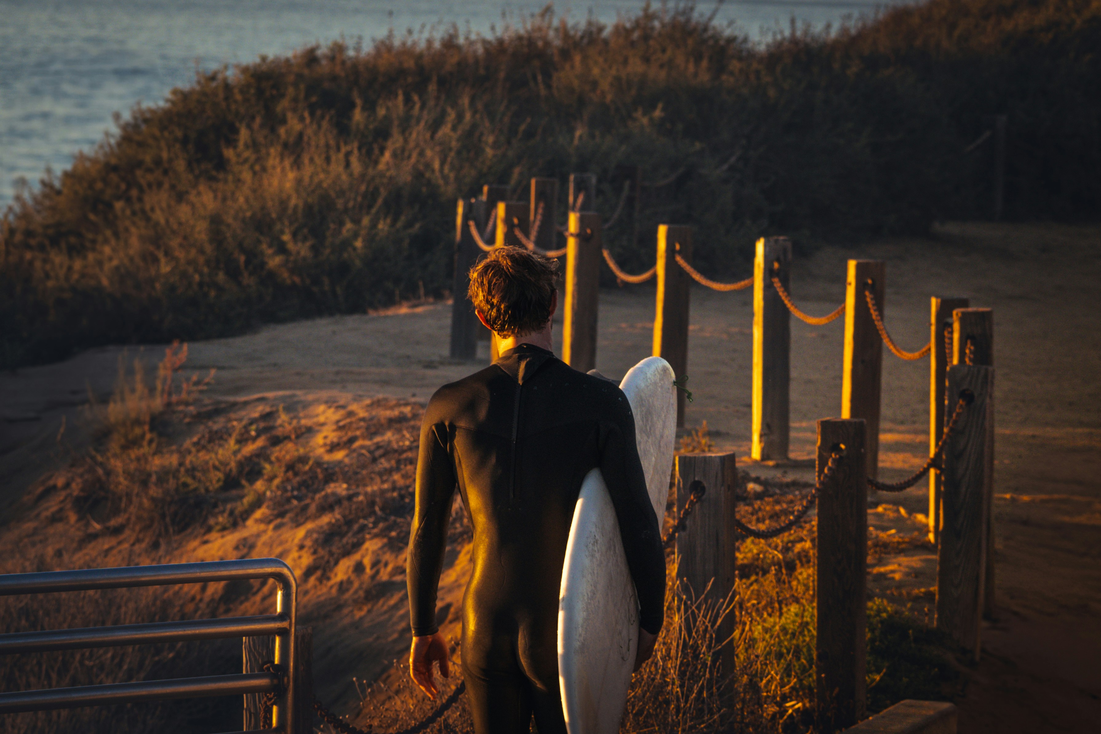 Surf Rider at Golden Hour: A lone surfer heads toward the path to the sea