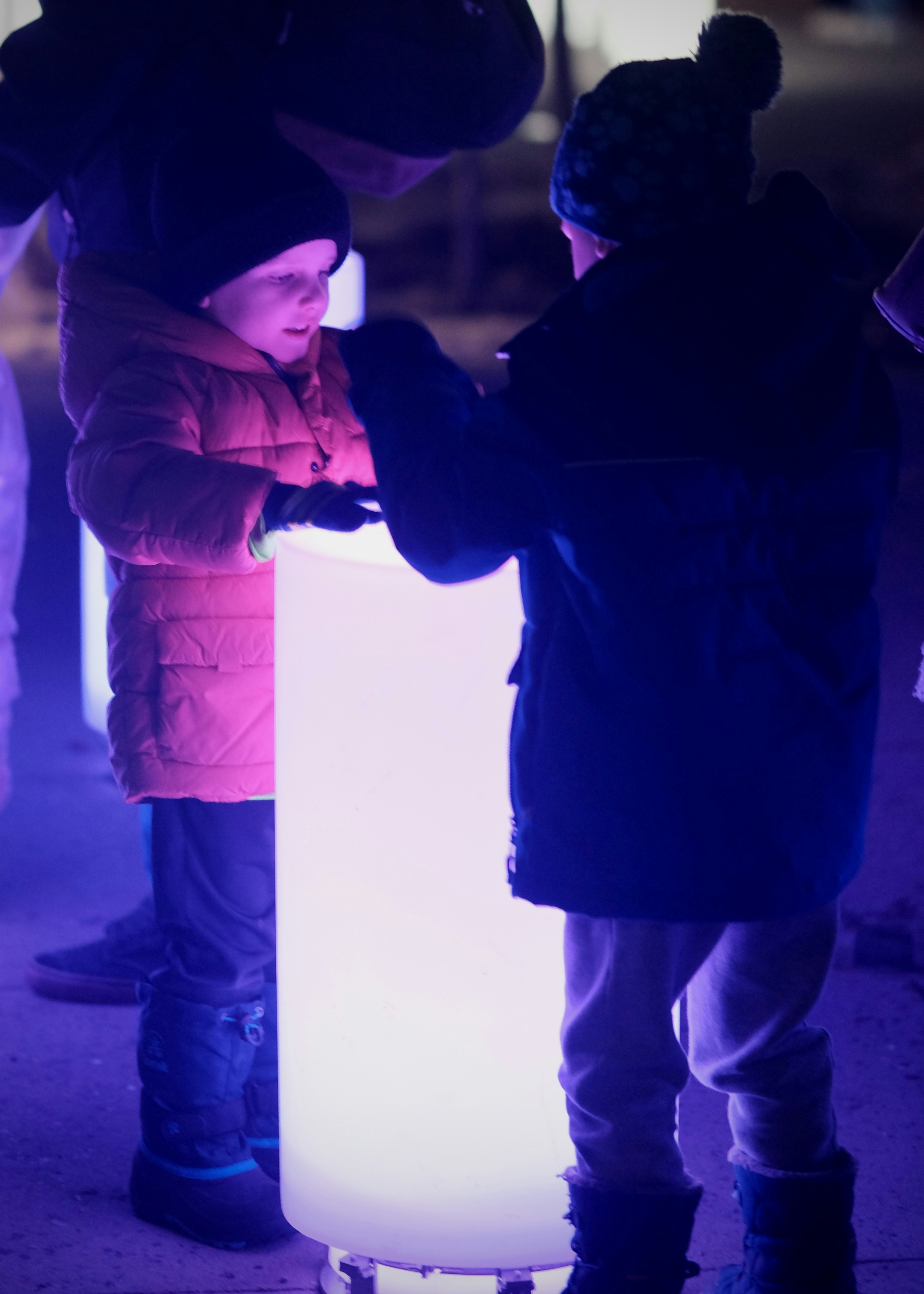 Children at a glowing ice lantern, sharing a quiet moment