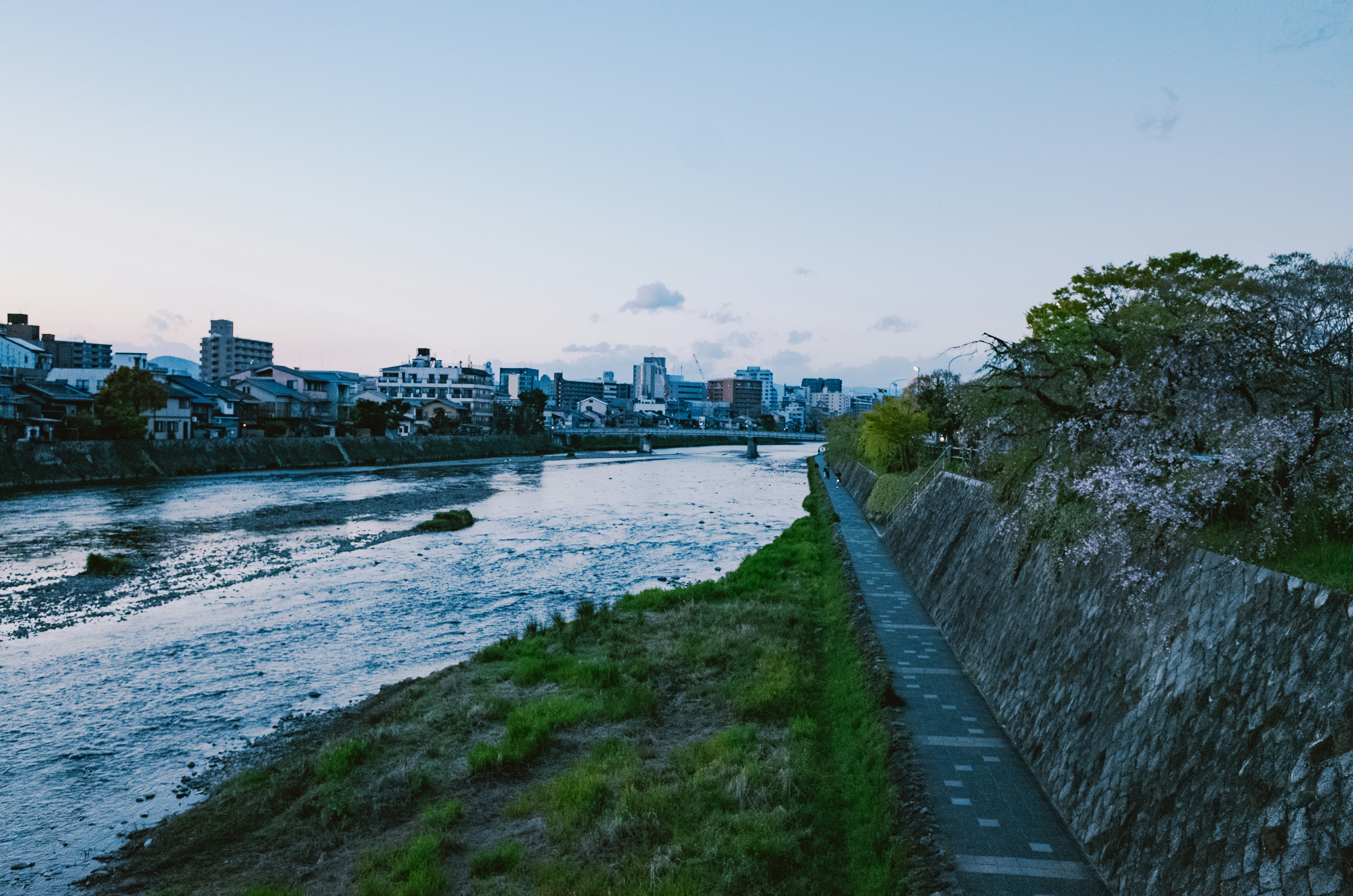 Riverside Pathway in Dusk: City Horizon and Stone Embankment