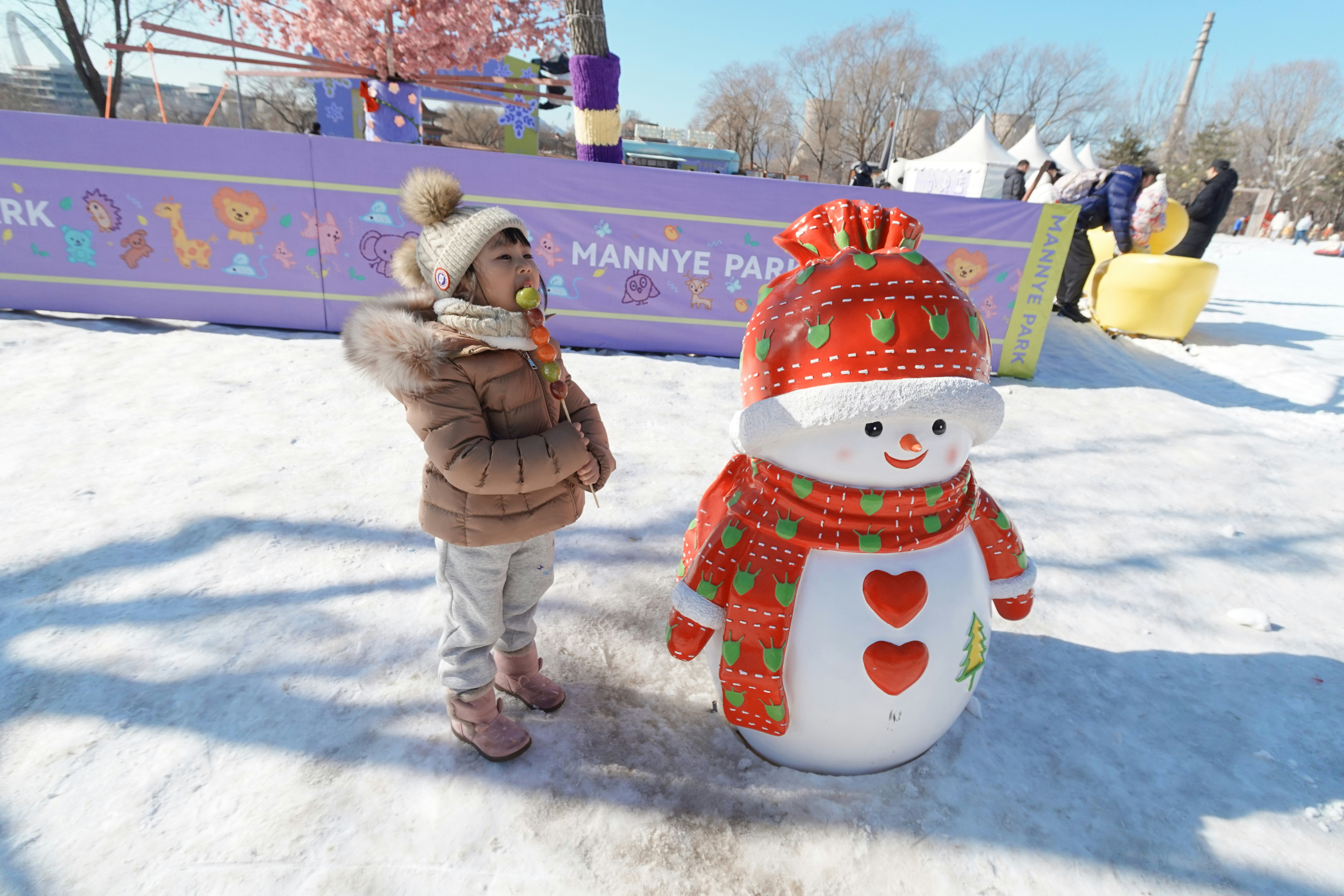 A child stands next to a snowman decoration.