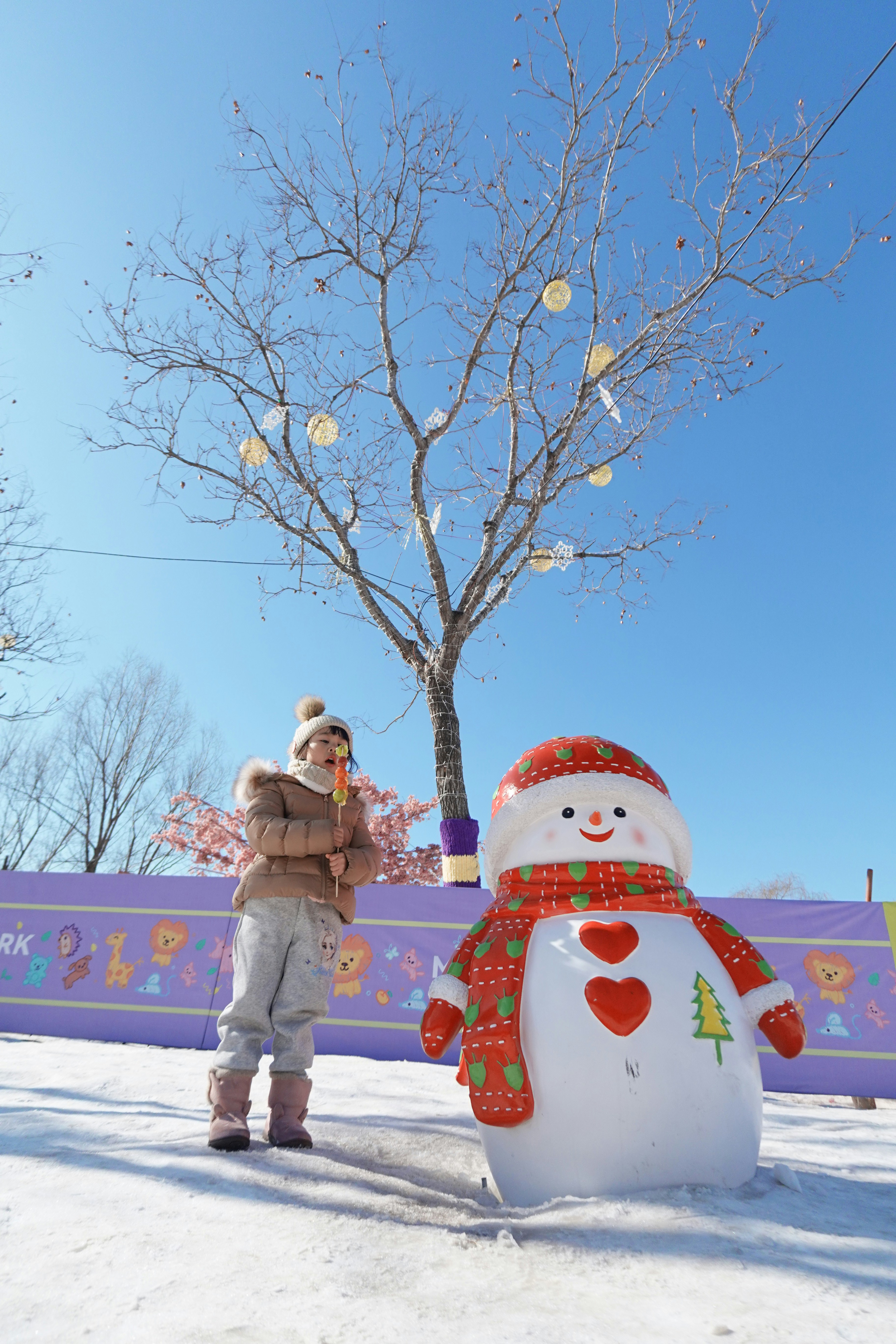 A child stands by a large snowman decoration