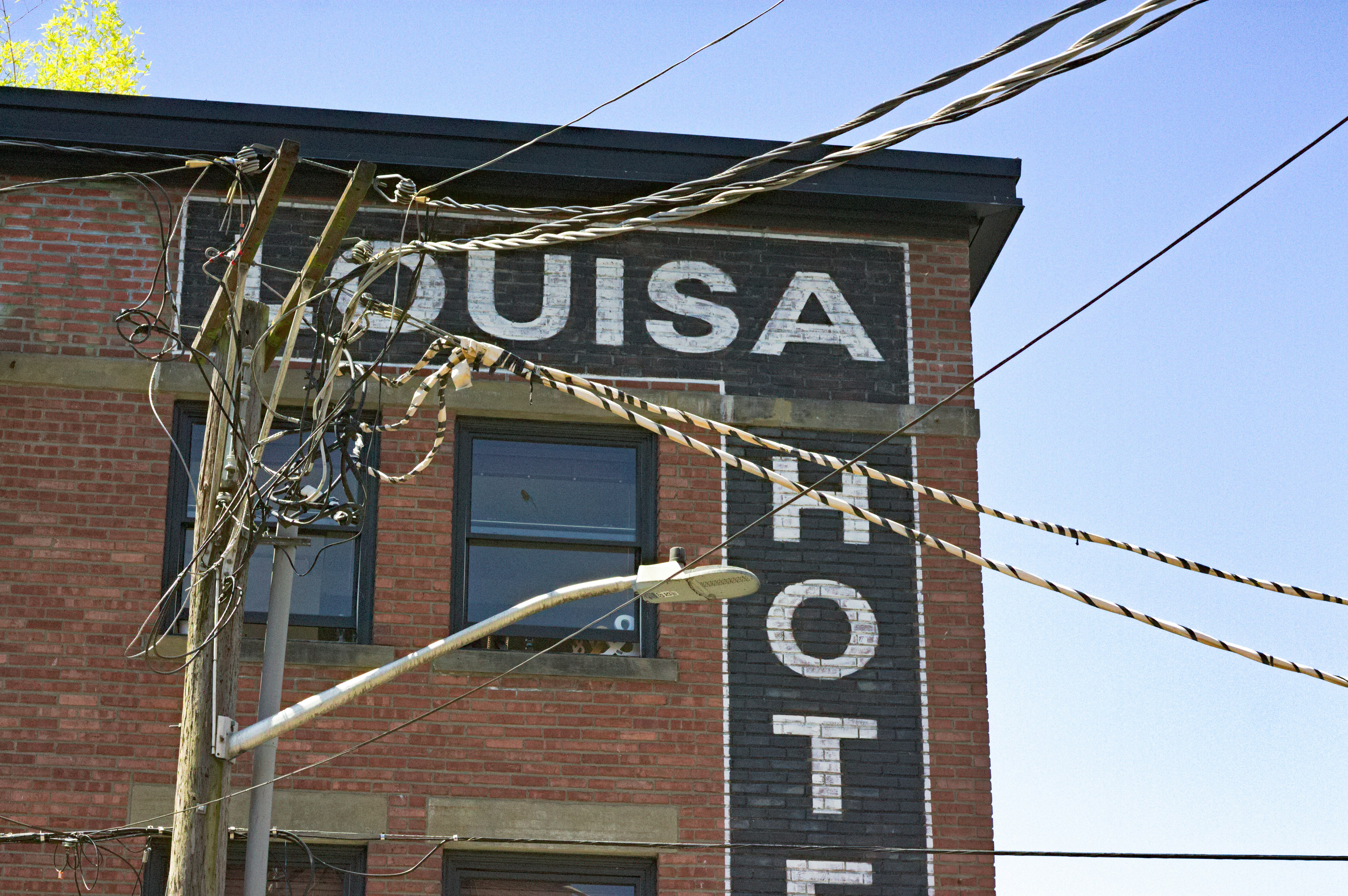 Brick hotel facade with vertical sign: LOUI SA HOTEL on the corner of a street