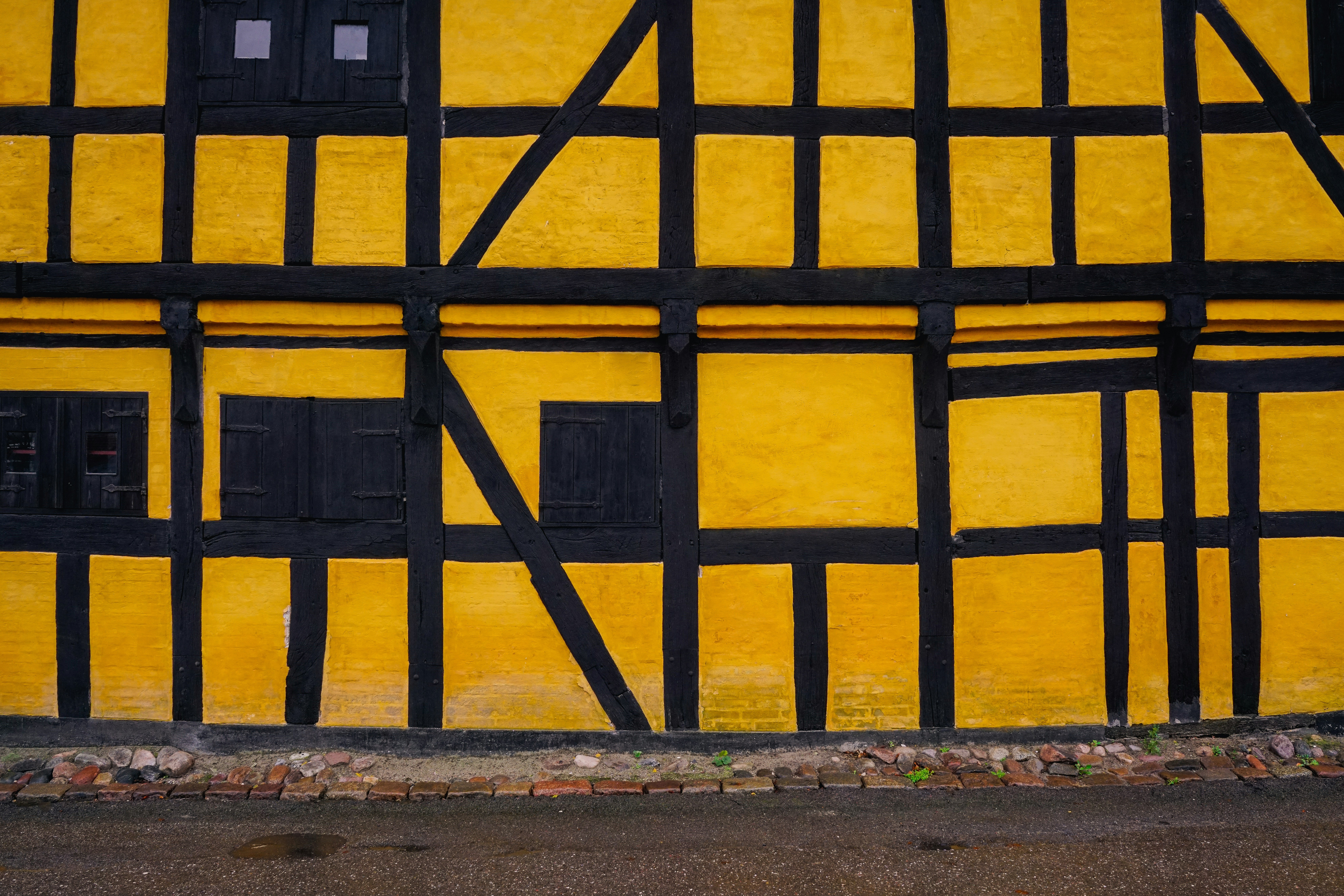 Yellow Timber-Framed Facade: Bold Black Beams on a Sunlit Wall