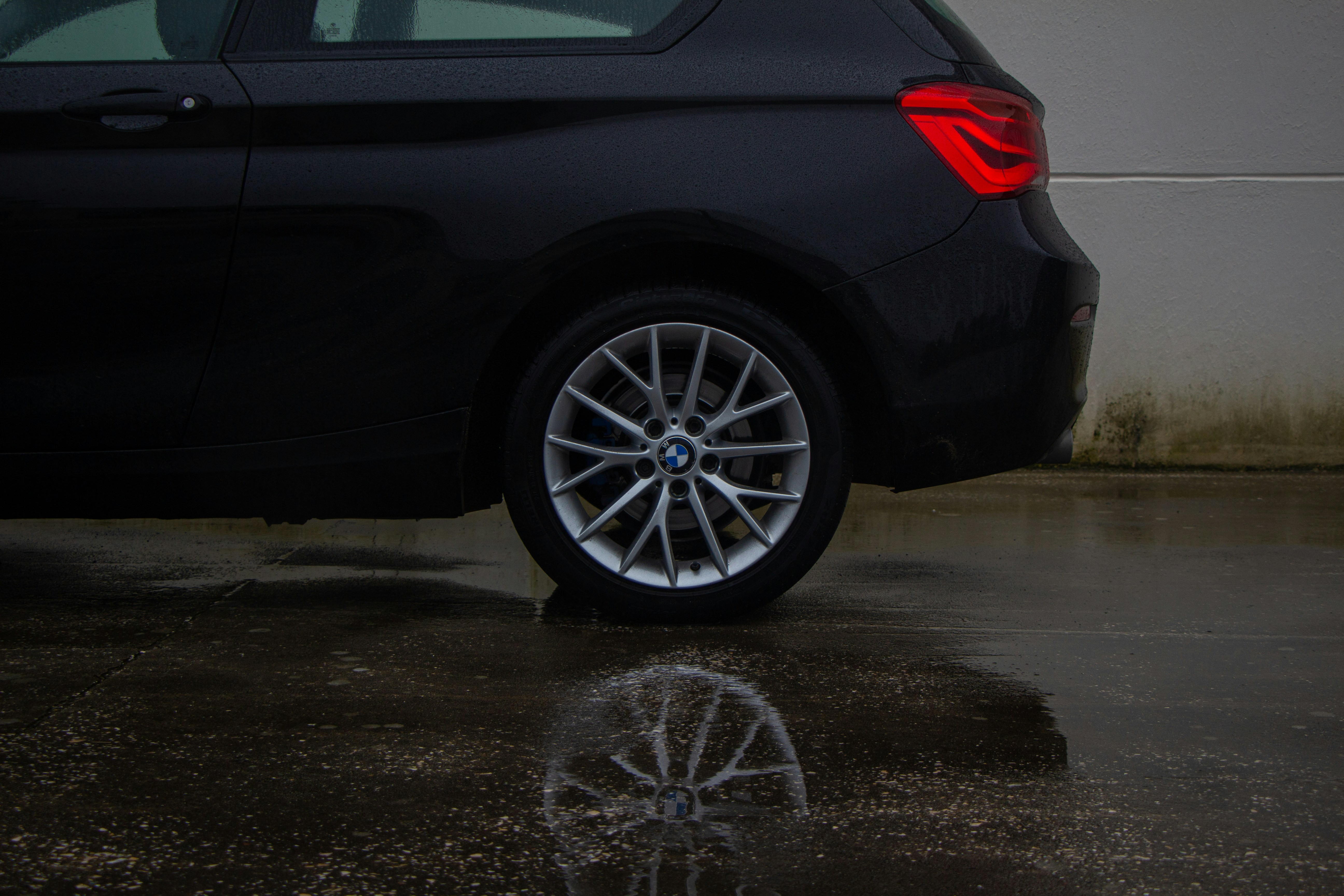 Rear-wheel Reflections: A Wet Parking Lot Under a Black BMW