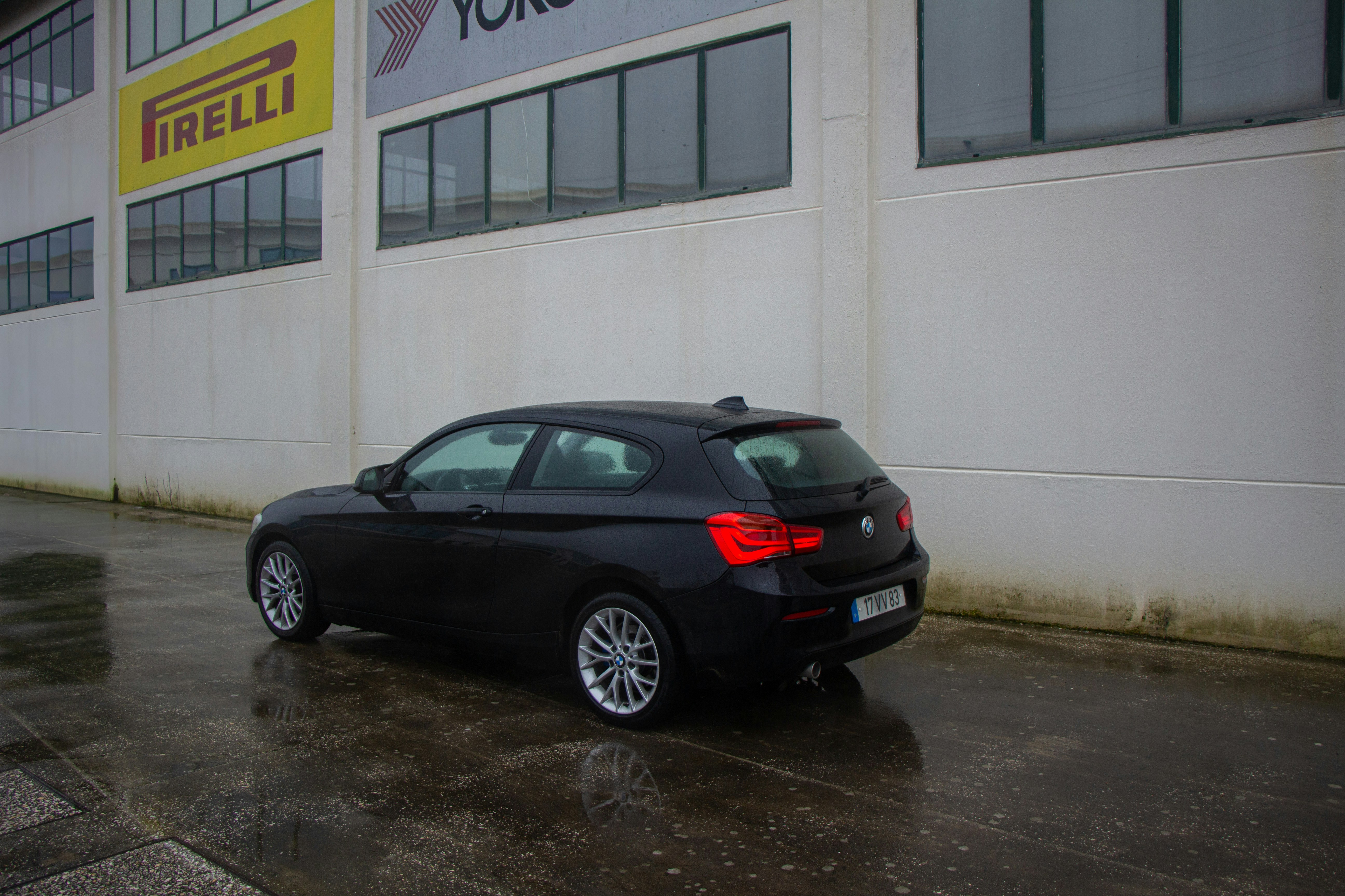 Black convertible hatchback parked beside a white industrial wall under overcast sky