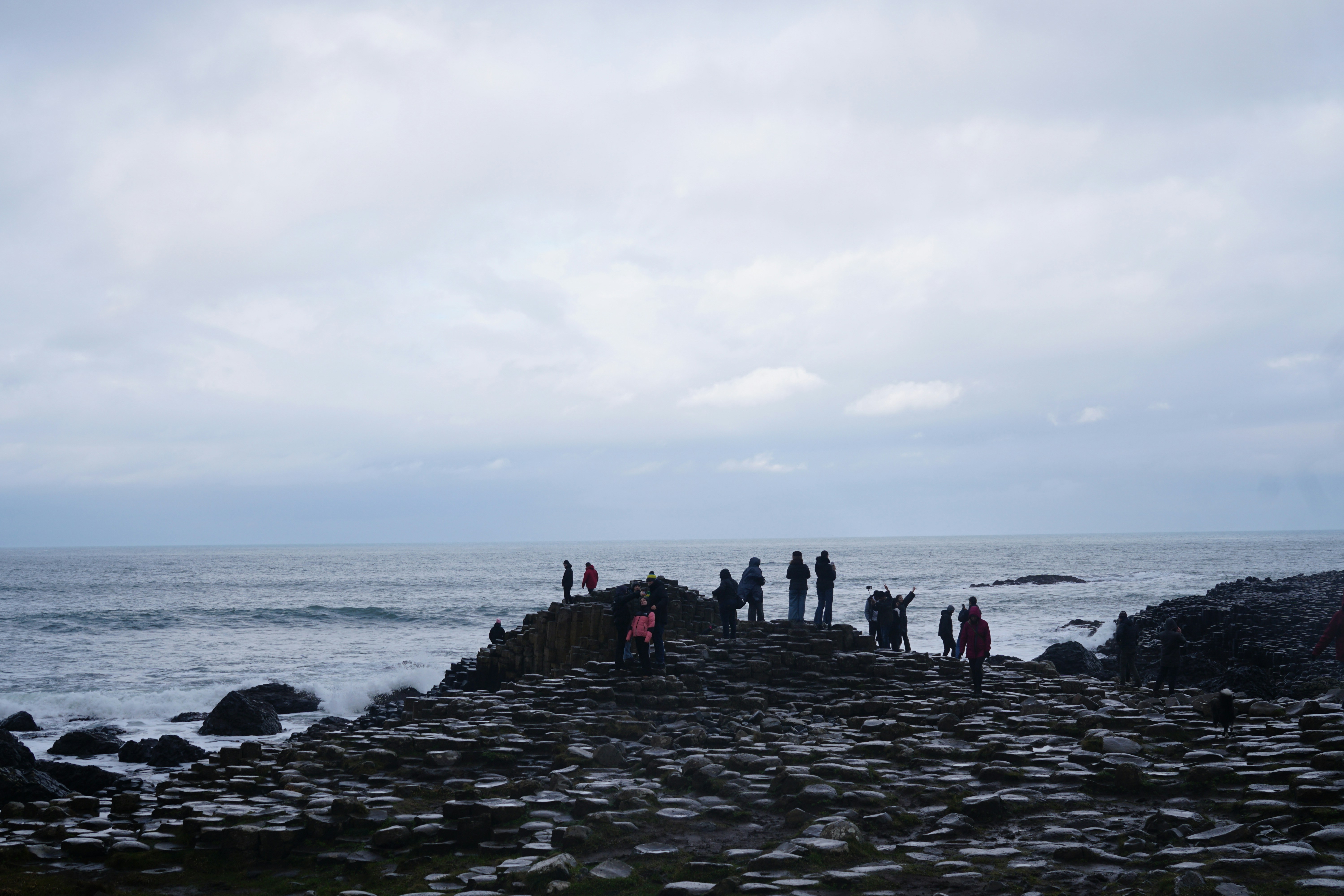 People on a rocky jetty extending into a calm sea at dusk