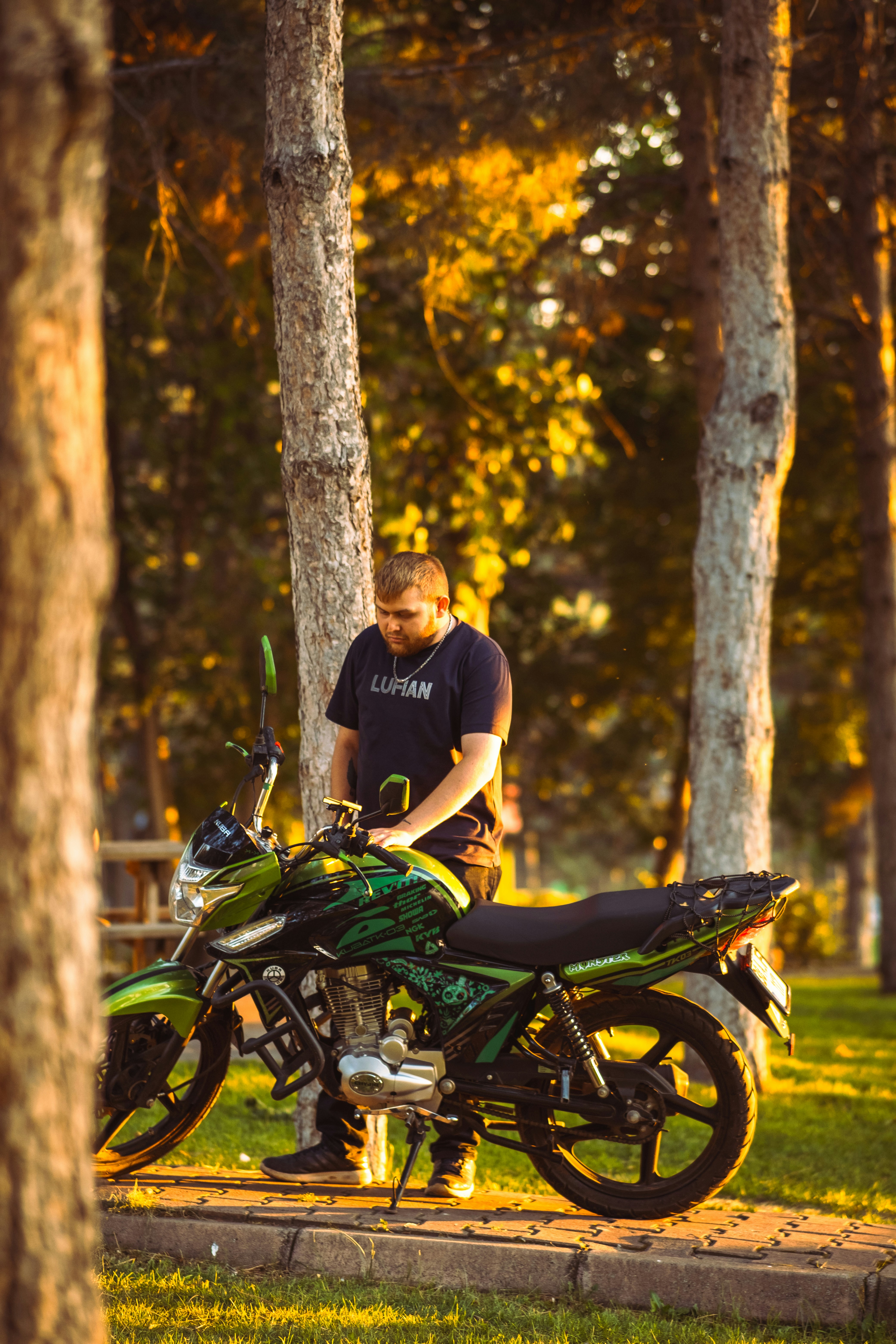 Motorcycle in a sunlit park: man in navy shirt beside a green bike